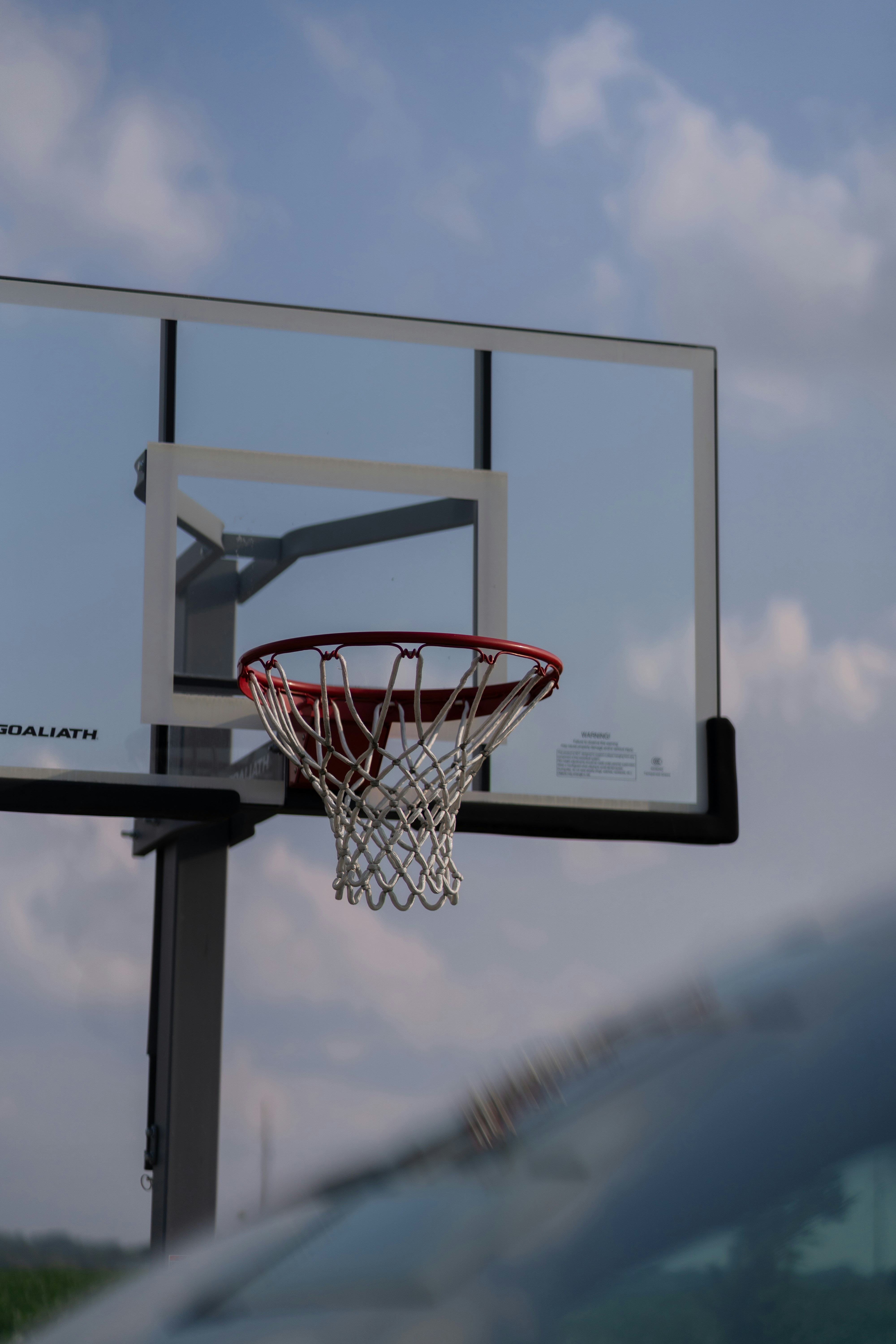 Basketball hoop with a clear backboard and a blue sky.