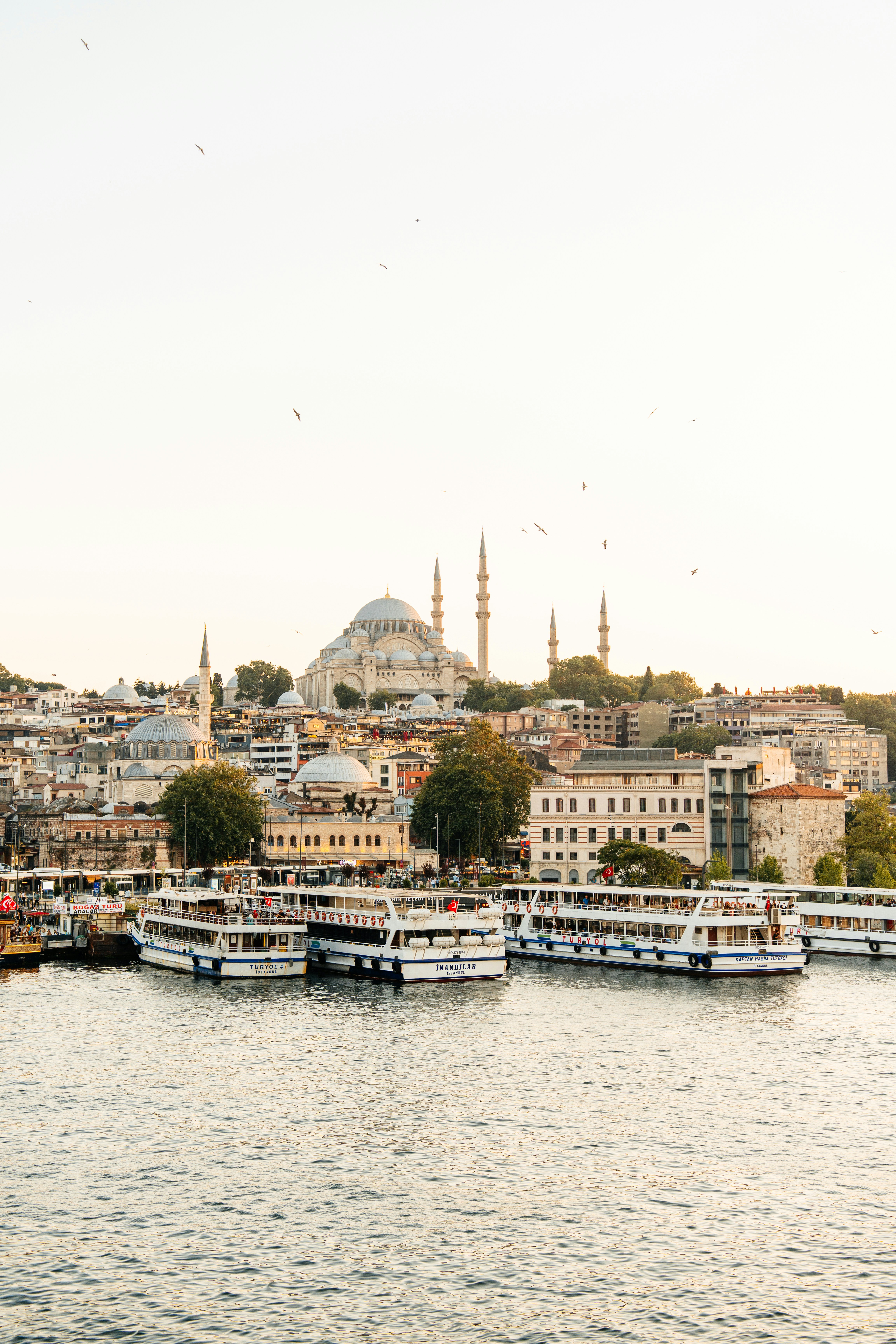 Bustling boats lined along the waterfront with the majestic skyline of Istanbul featuring domes and minarets at sunset.