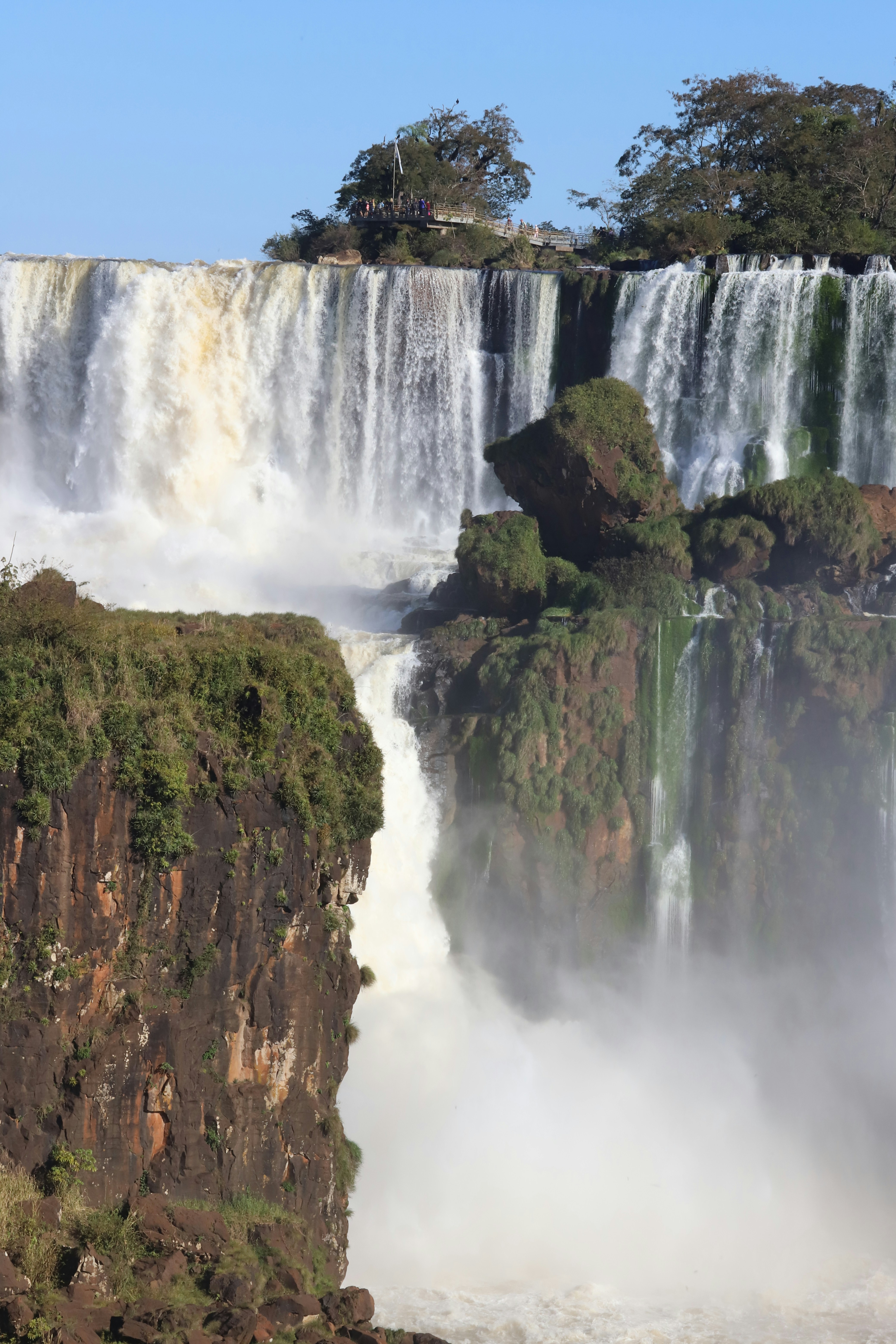 Powerful waterfall cascading over rocky cliffs, surrounded by lush greenery and mist rising from the base.
