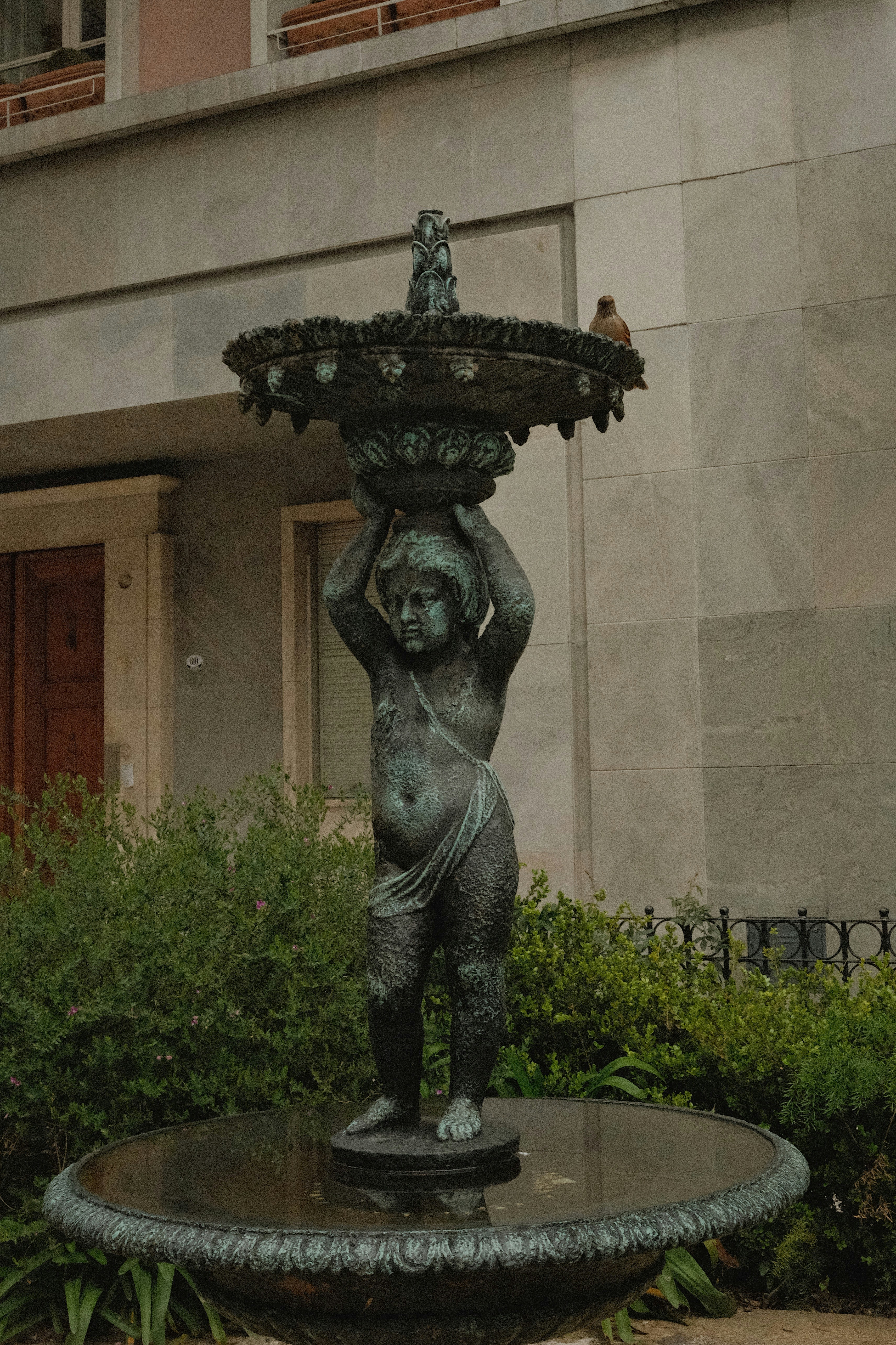 A bronze fountain features a child-like statue.