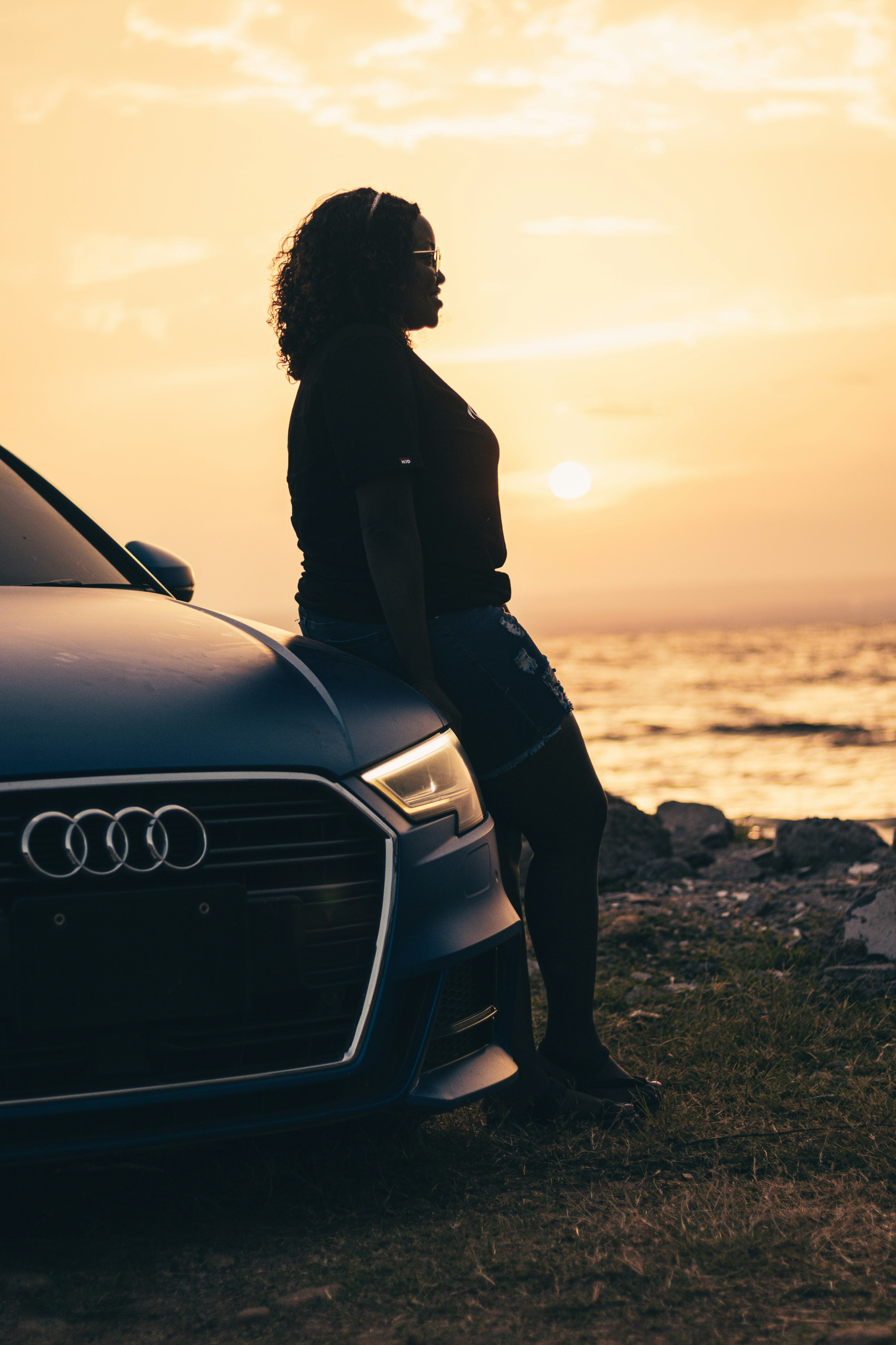 Silhouette at Sunset: A Woman Leaning on an Audi by the Sea