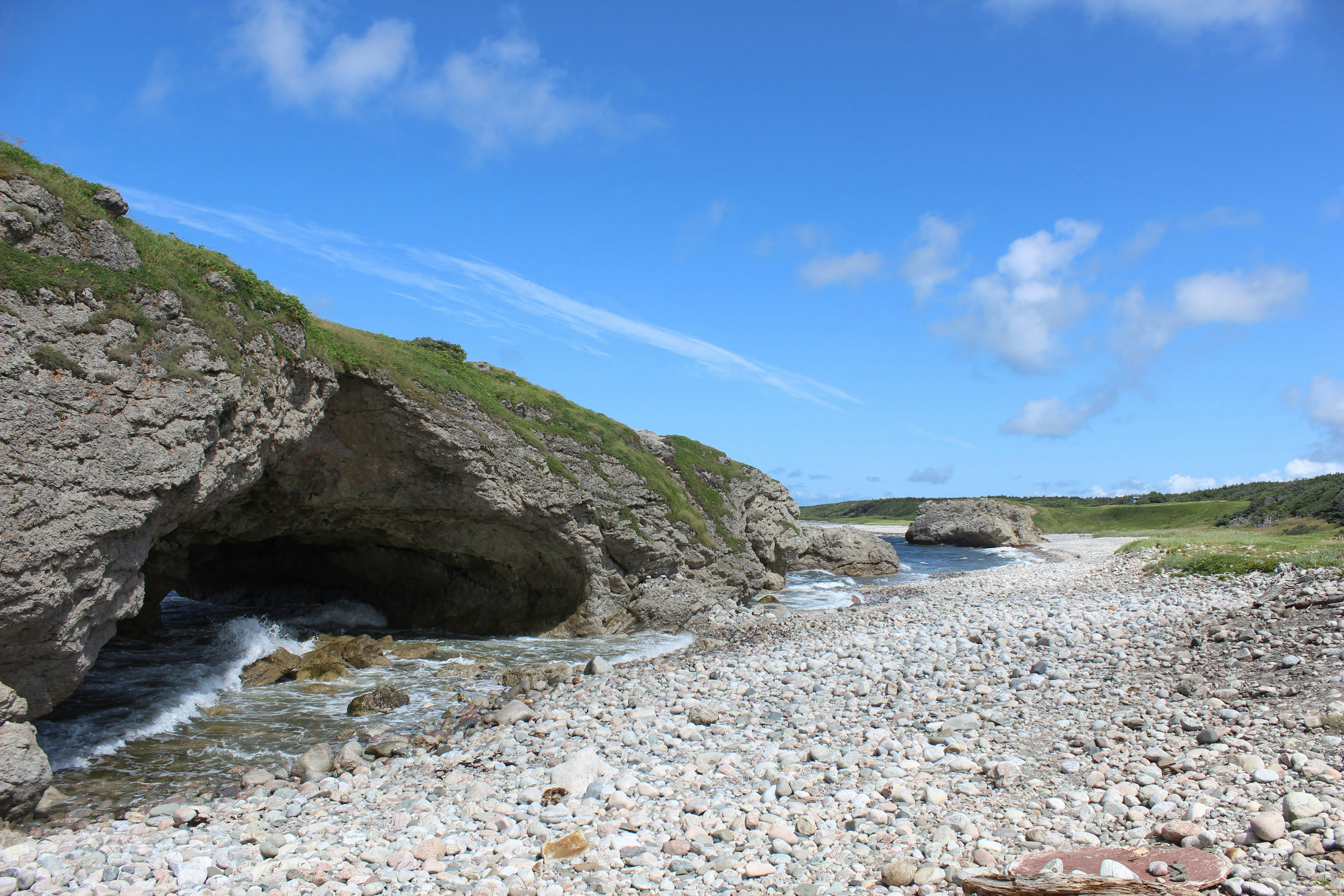 Looking at the Arches in Arches Provincial Park on a sunny day. Aug 2023. | A cave overlooks the ocean with a bright blue sky.