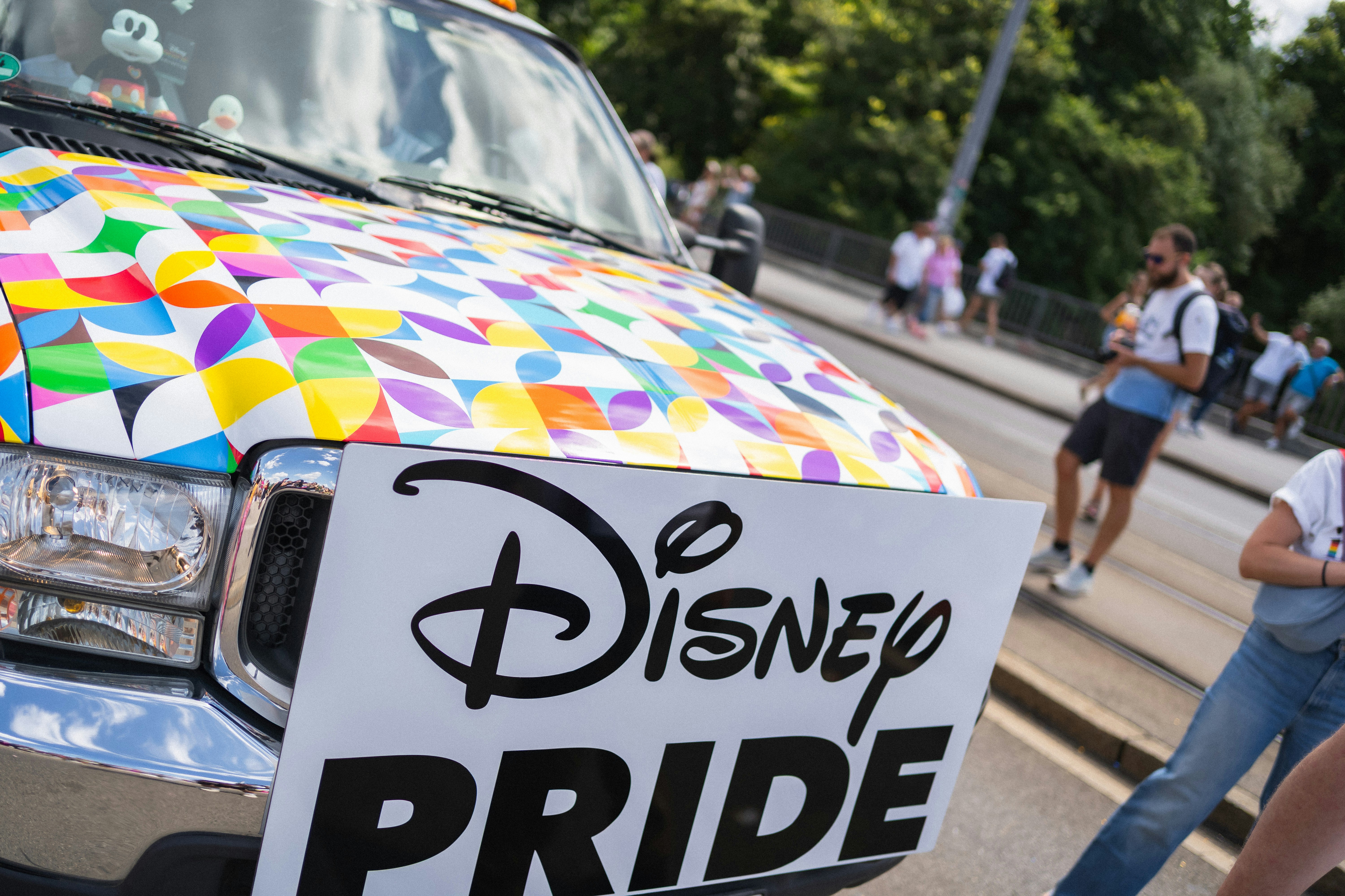 Colorful vehicle adorned with a playful design and a prominent Disney Pride sign at a lively event.