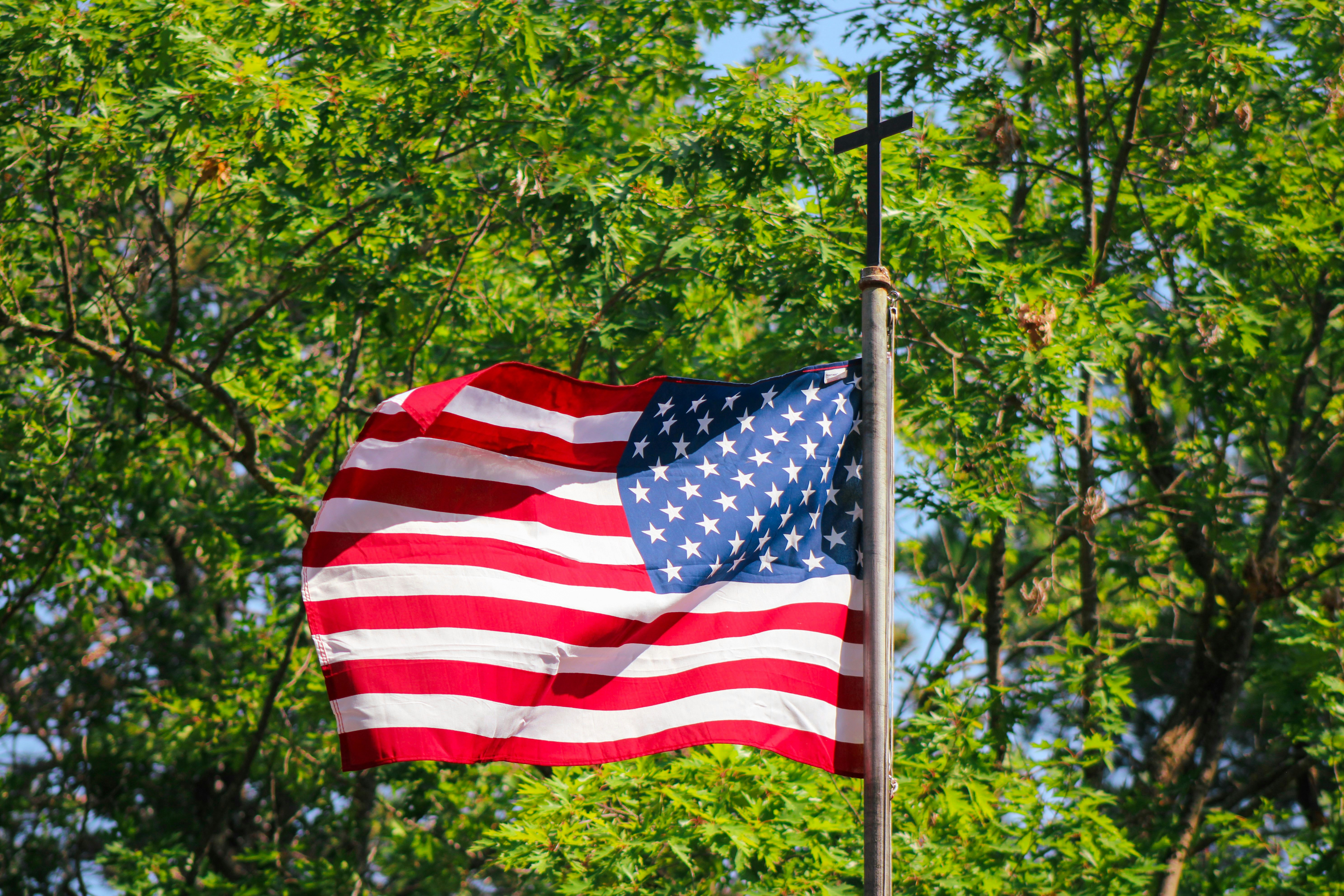 For God and Country | The american flag waves proudly with a cross.