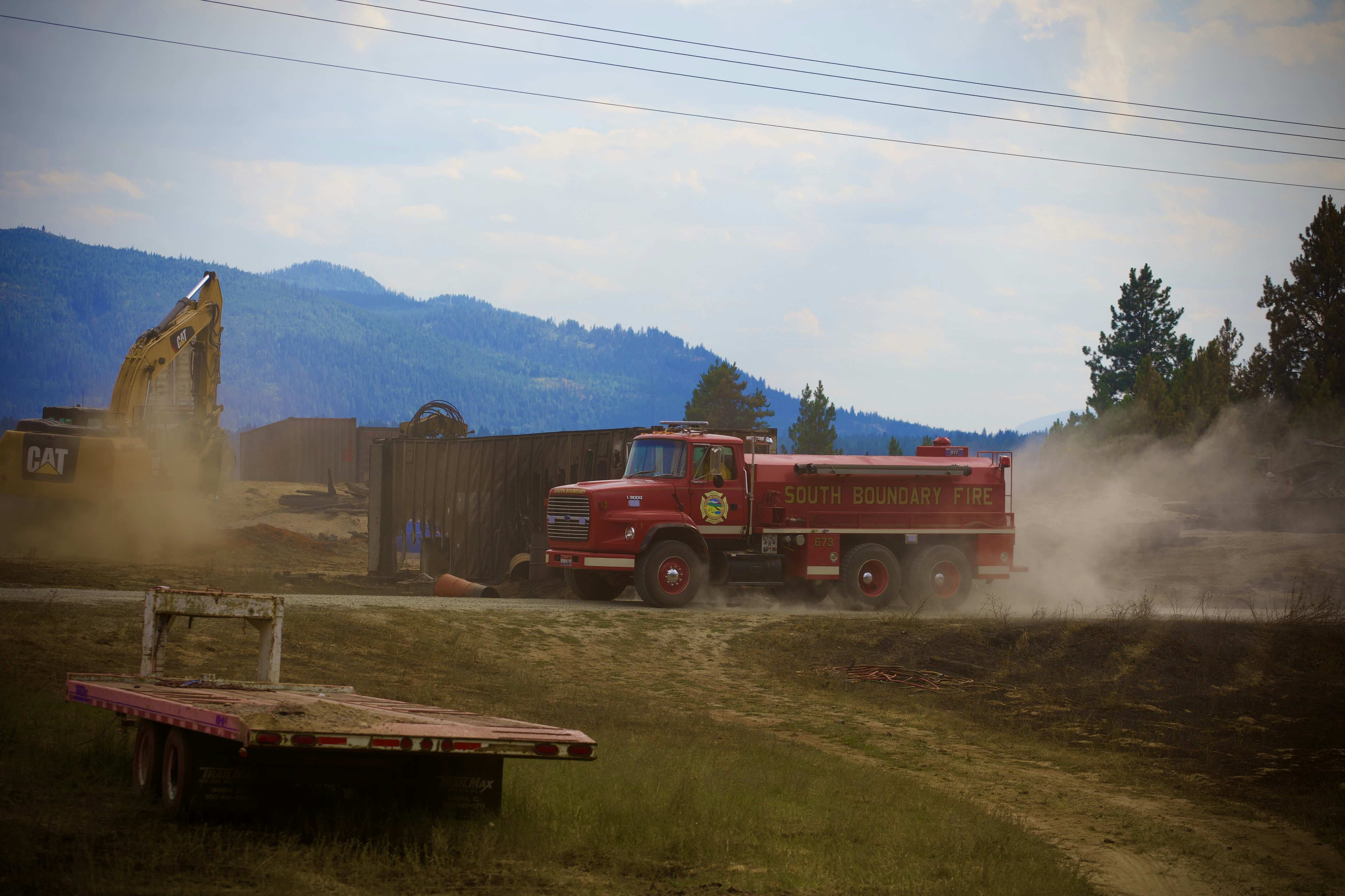 Red Engine in a Dusty Yard: Machinery, Mud, and Mountain Backdrop