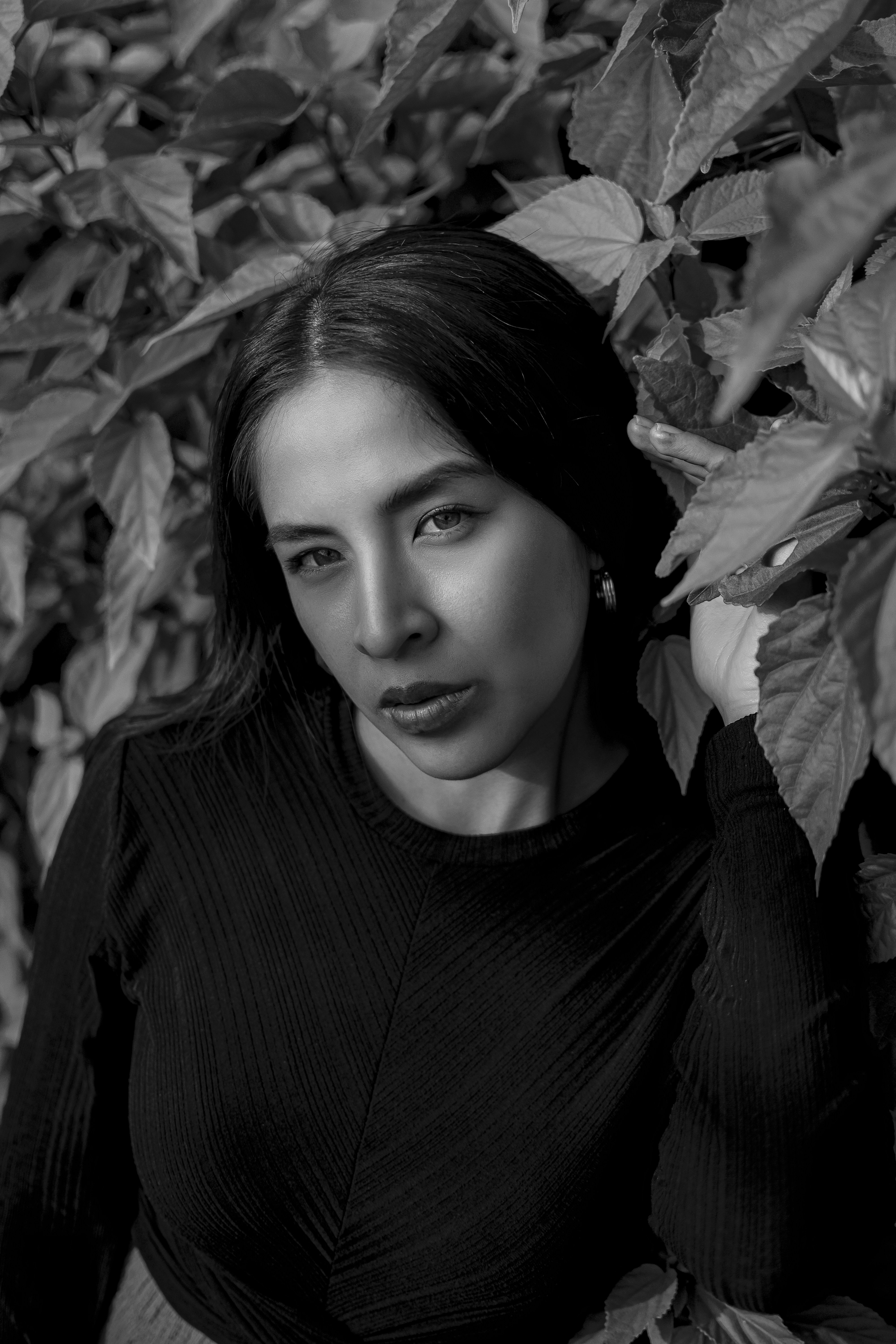 Woman poses near lush foliage in black and white.