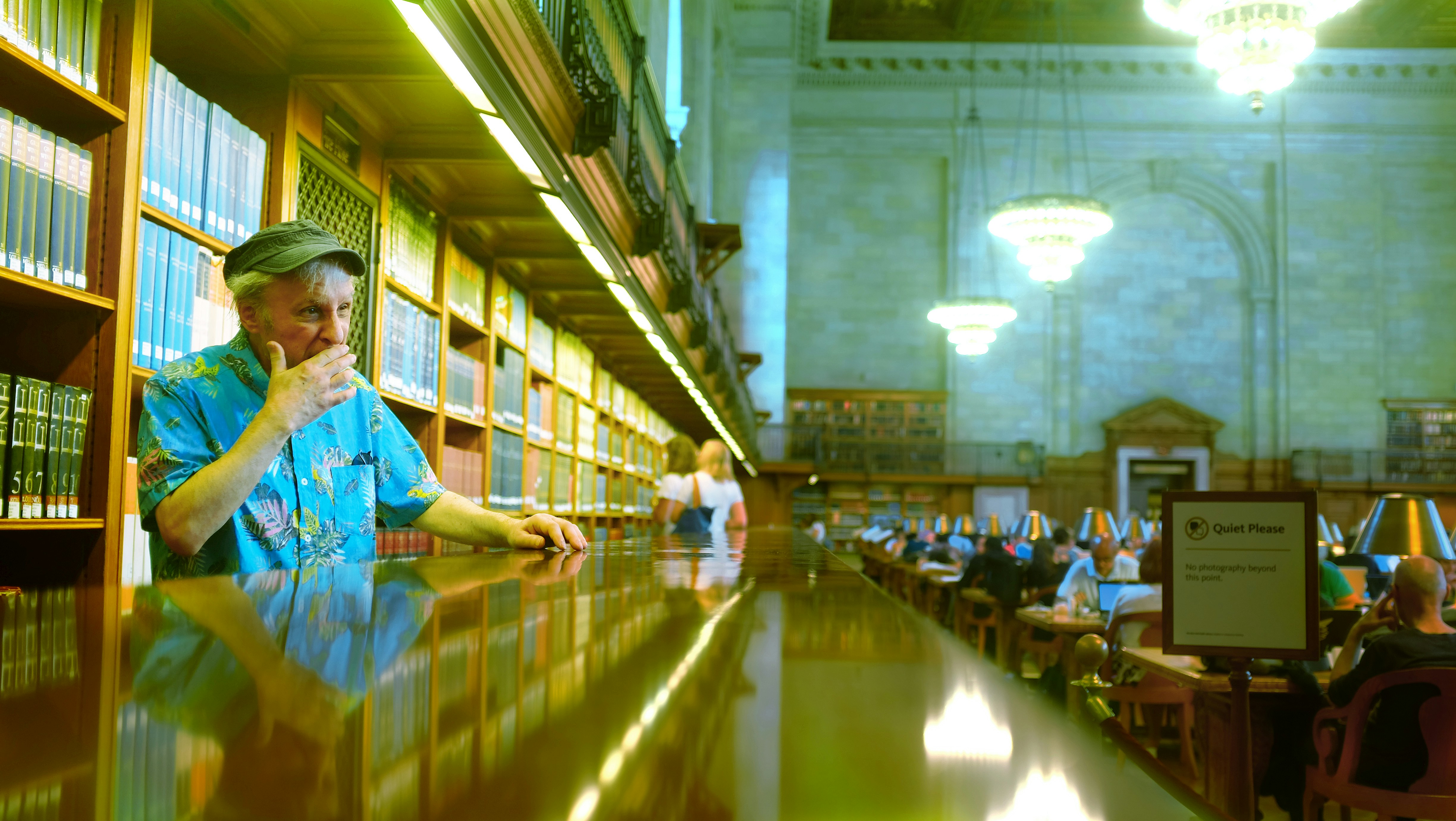 A thoughtful man pauses at a polished wooden table in a grand library, surrounded by shelves of books and soft, ambient lighting.
