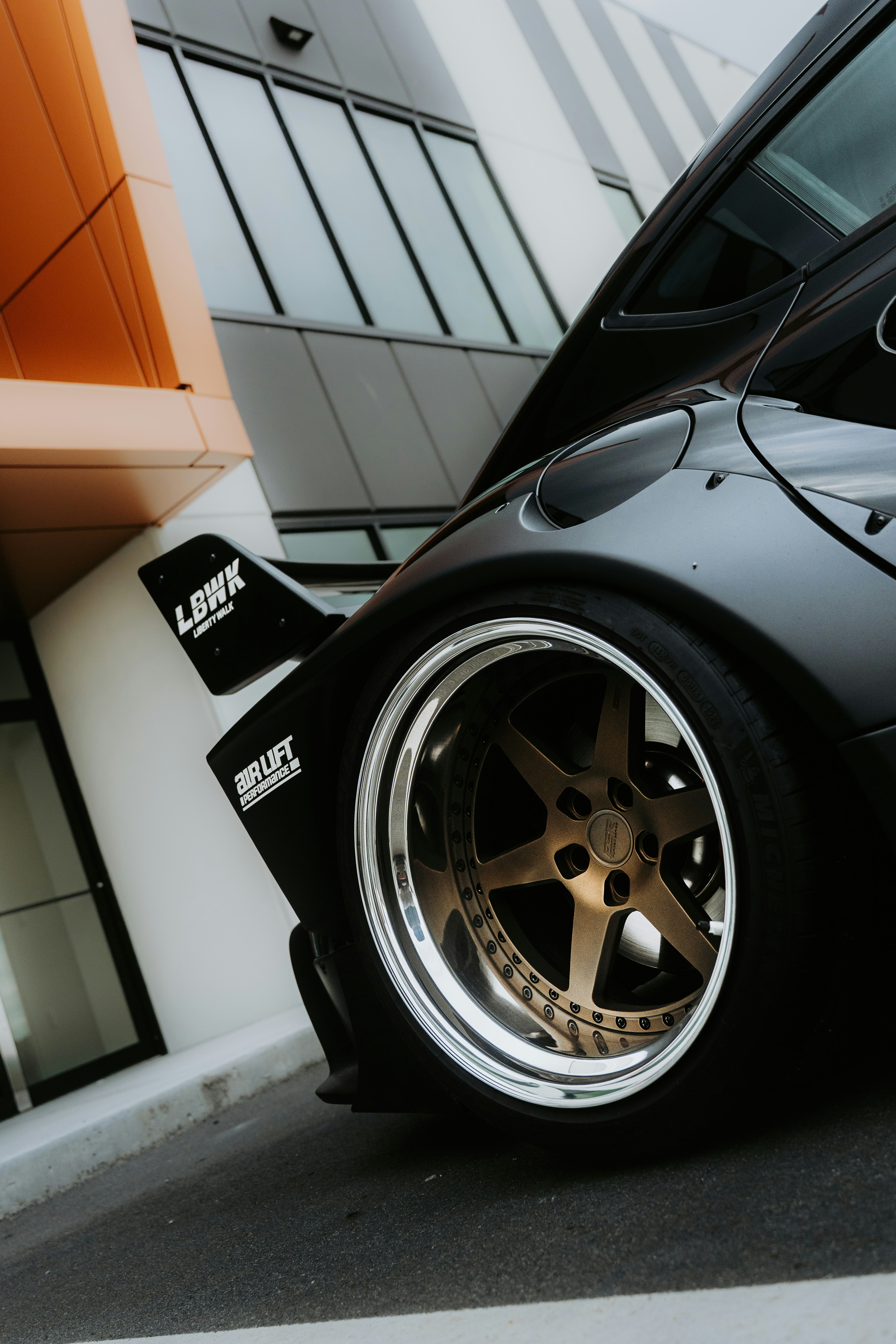 Low-angle view of a modified car showcasing its sleek wheel design and aerodynamic features against a modern architectural backdrop.