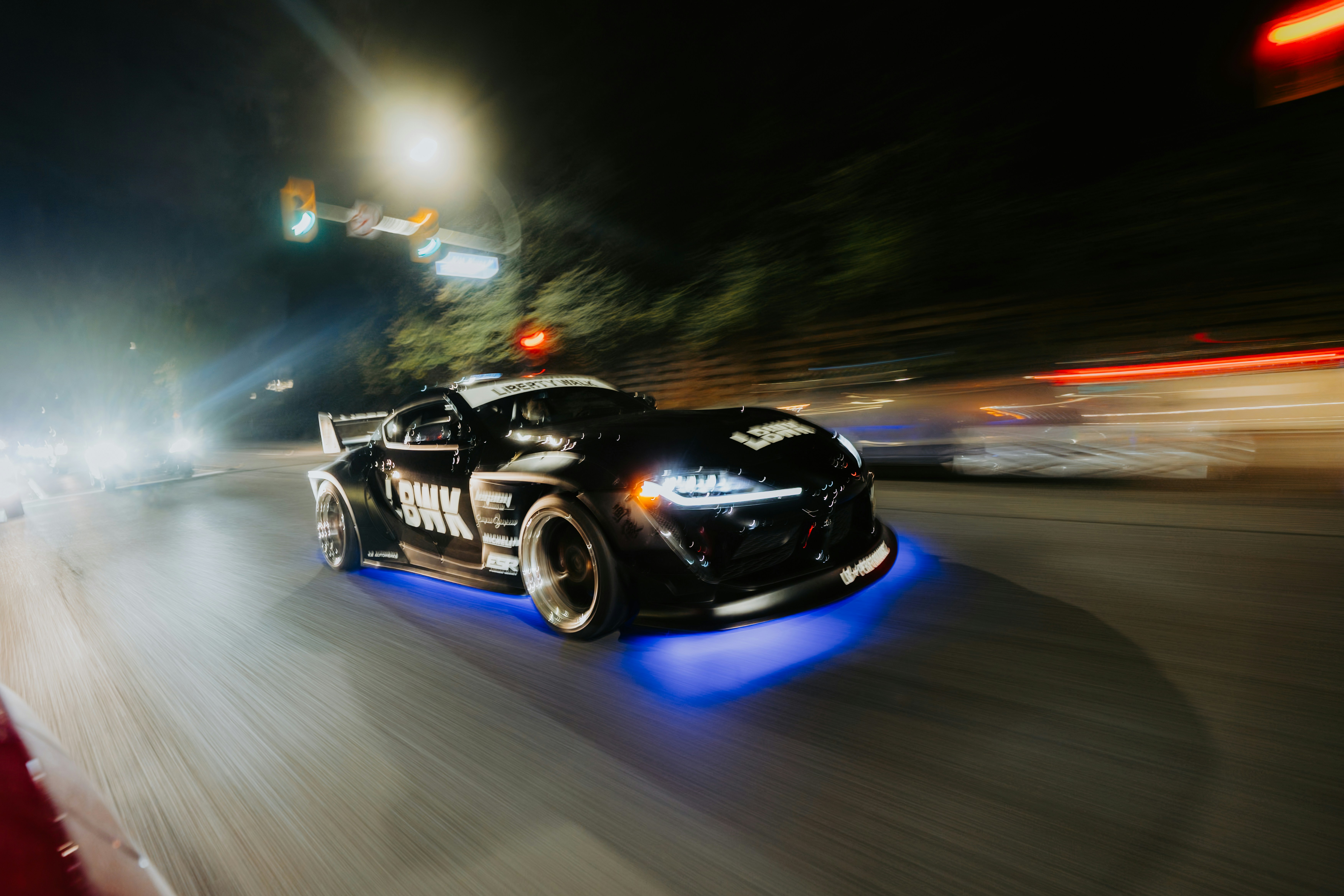 A high-performance car with glowing blue underlights races down a city street at night, capturing the essence of automotive adrenaline.