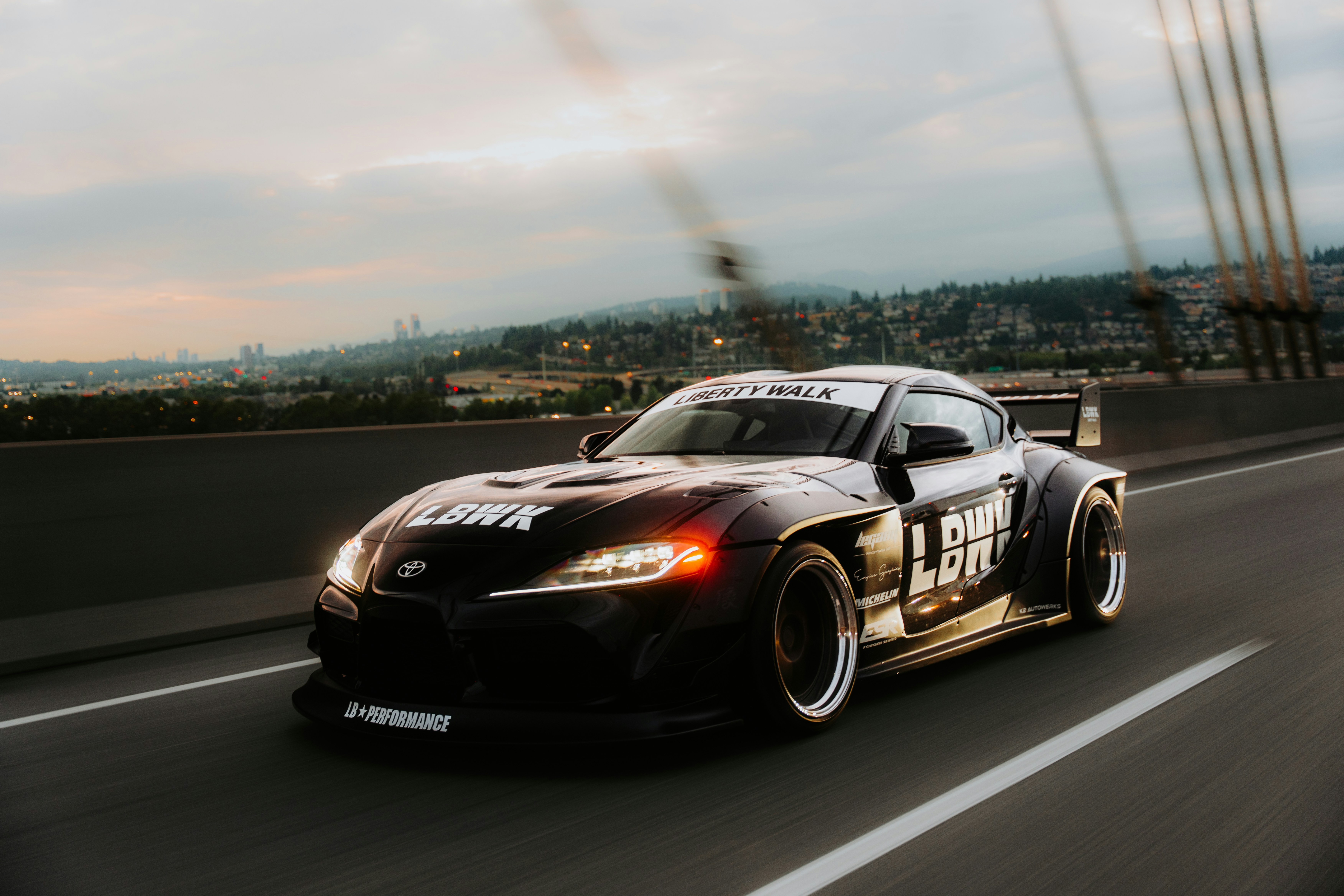 Modified sports car racing along a highway at dusk, showcasing dynamic lines and vibrant branding.