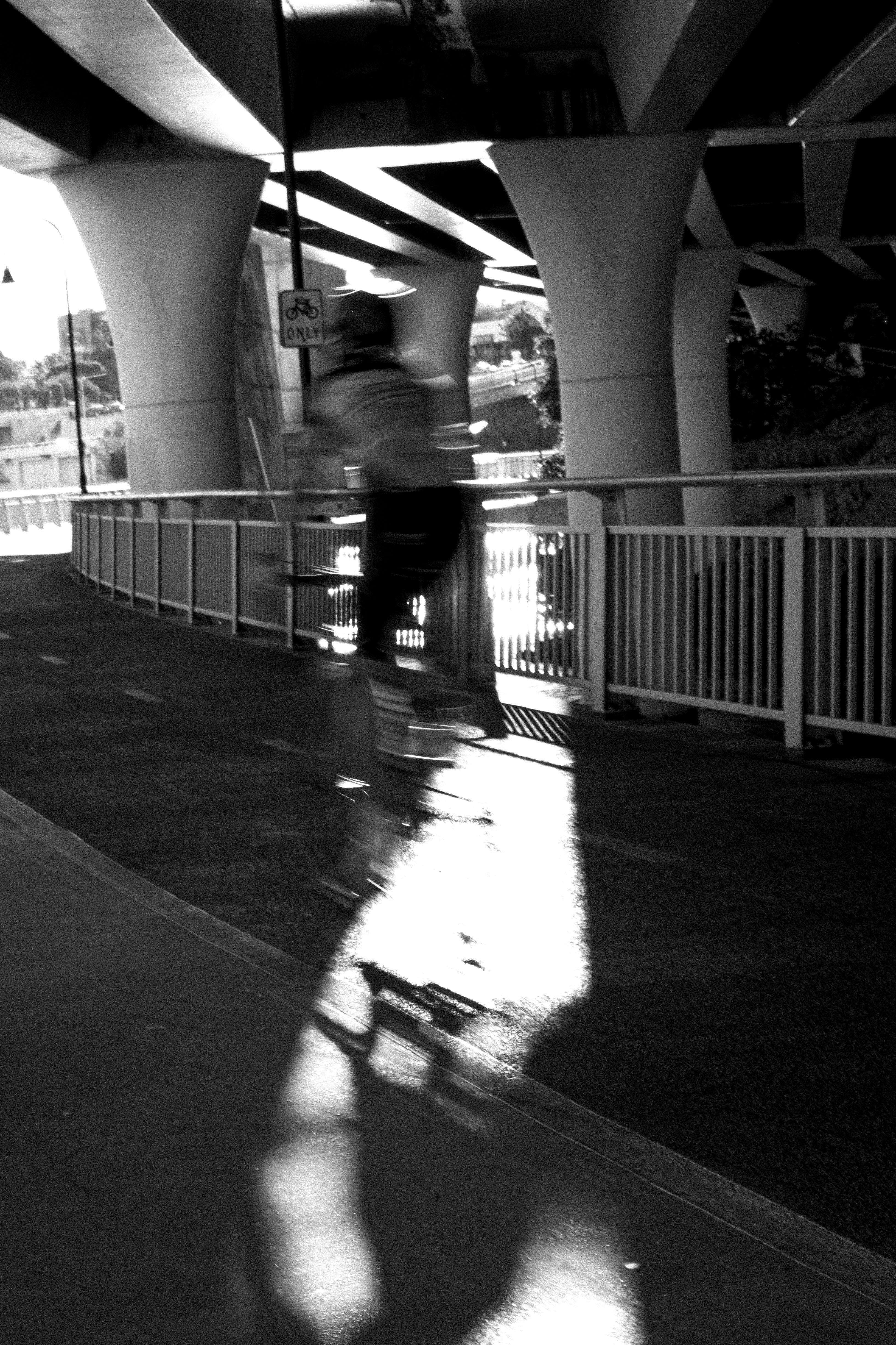 Bicyclist rides under the concrete overpass.