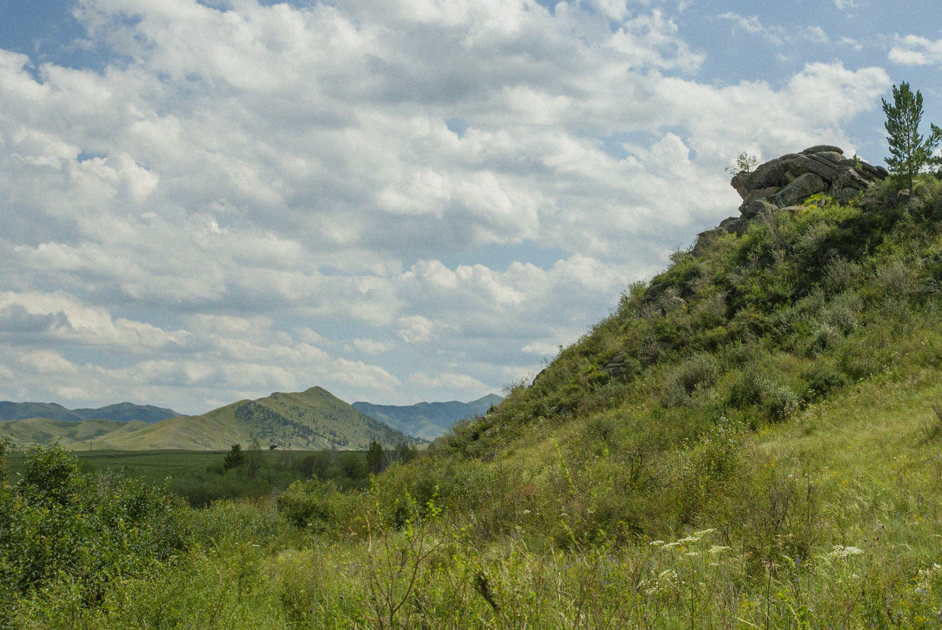 Lush green landscape with a rocky outcrop under a sky filled with scattered clouds, showcasing the tranquility of nature.