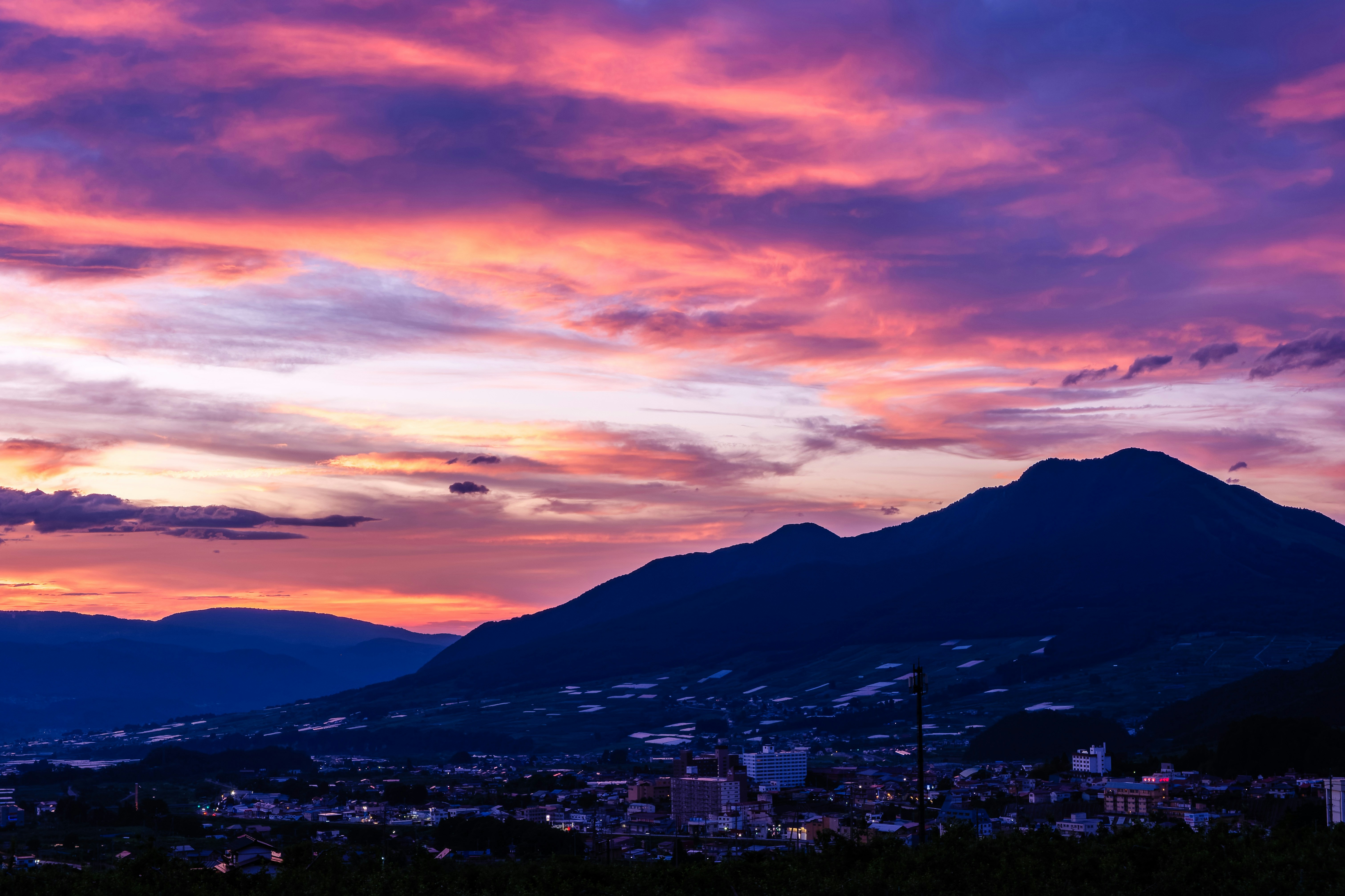 Vibrant sunset casting hues over a mountainous landscape, with a town illuminated in the foreground. 