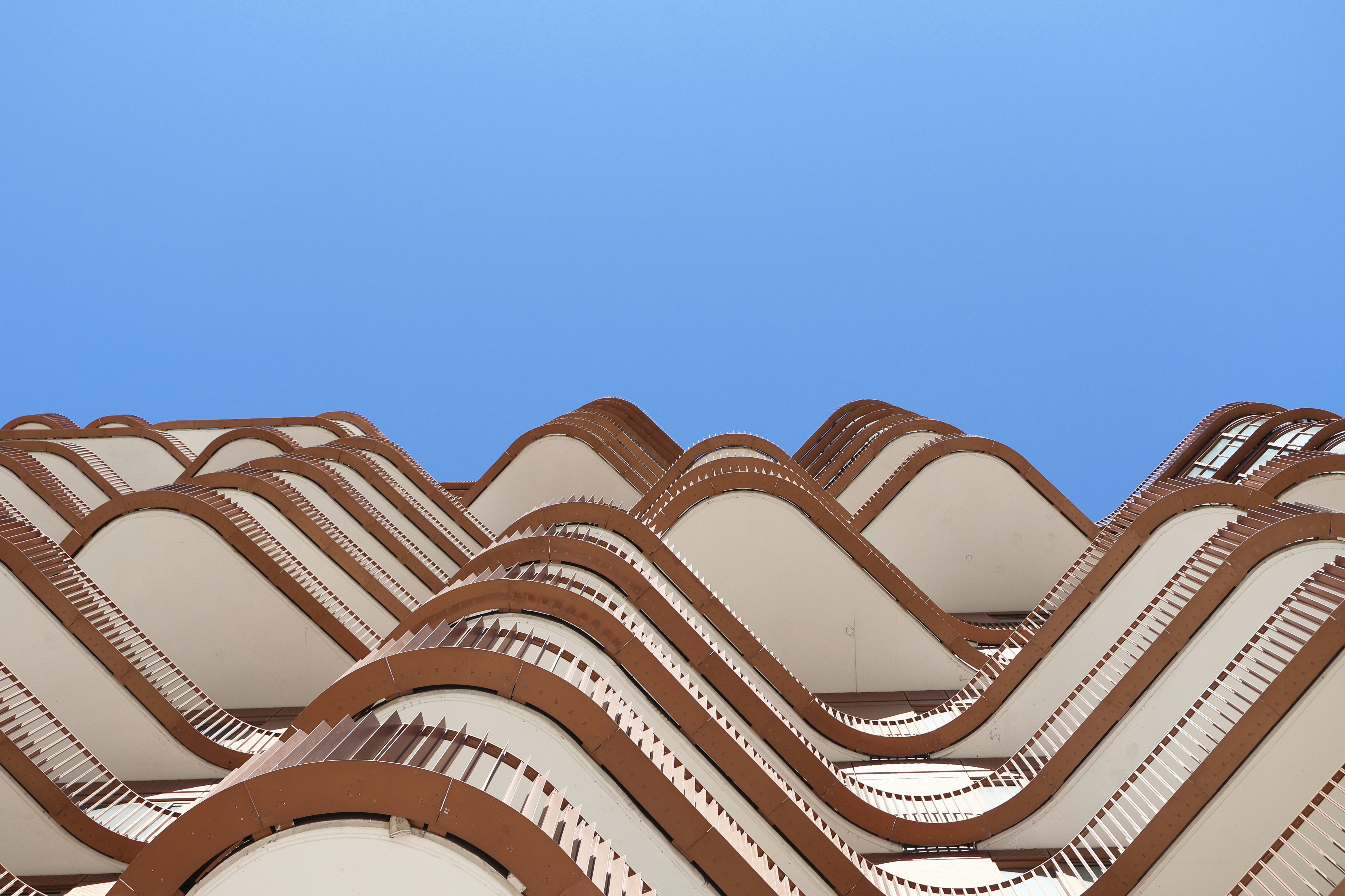 Modern white and brown architecture from below | Wavy architecture against a bright blue sky.