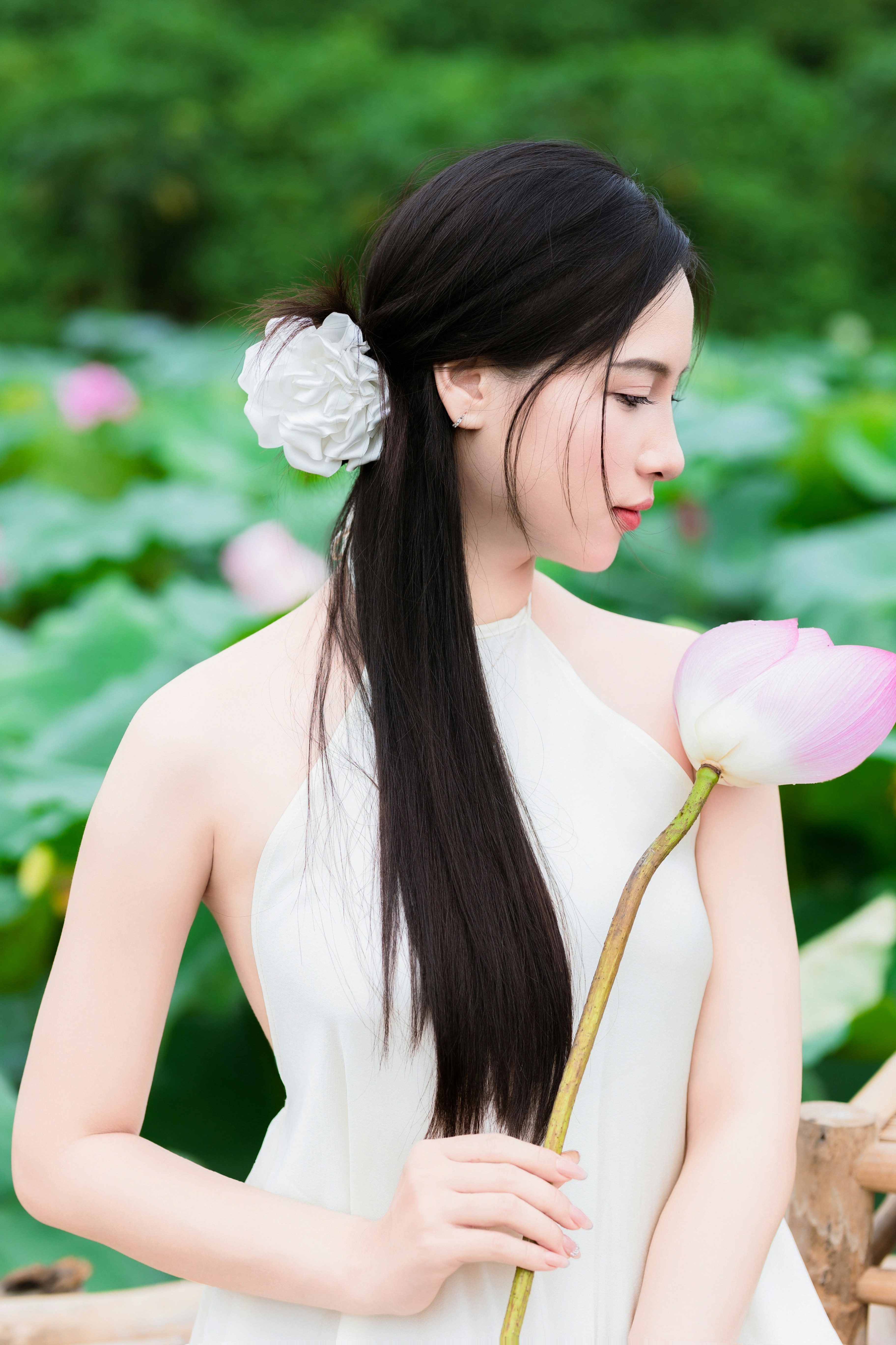 A serene figure in a flowing white dress holds a lotus flower, surrounded by lush green foliage and blooming lotus plants.