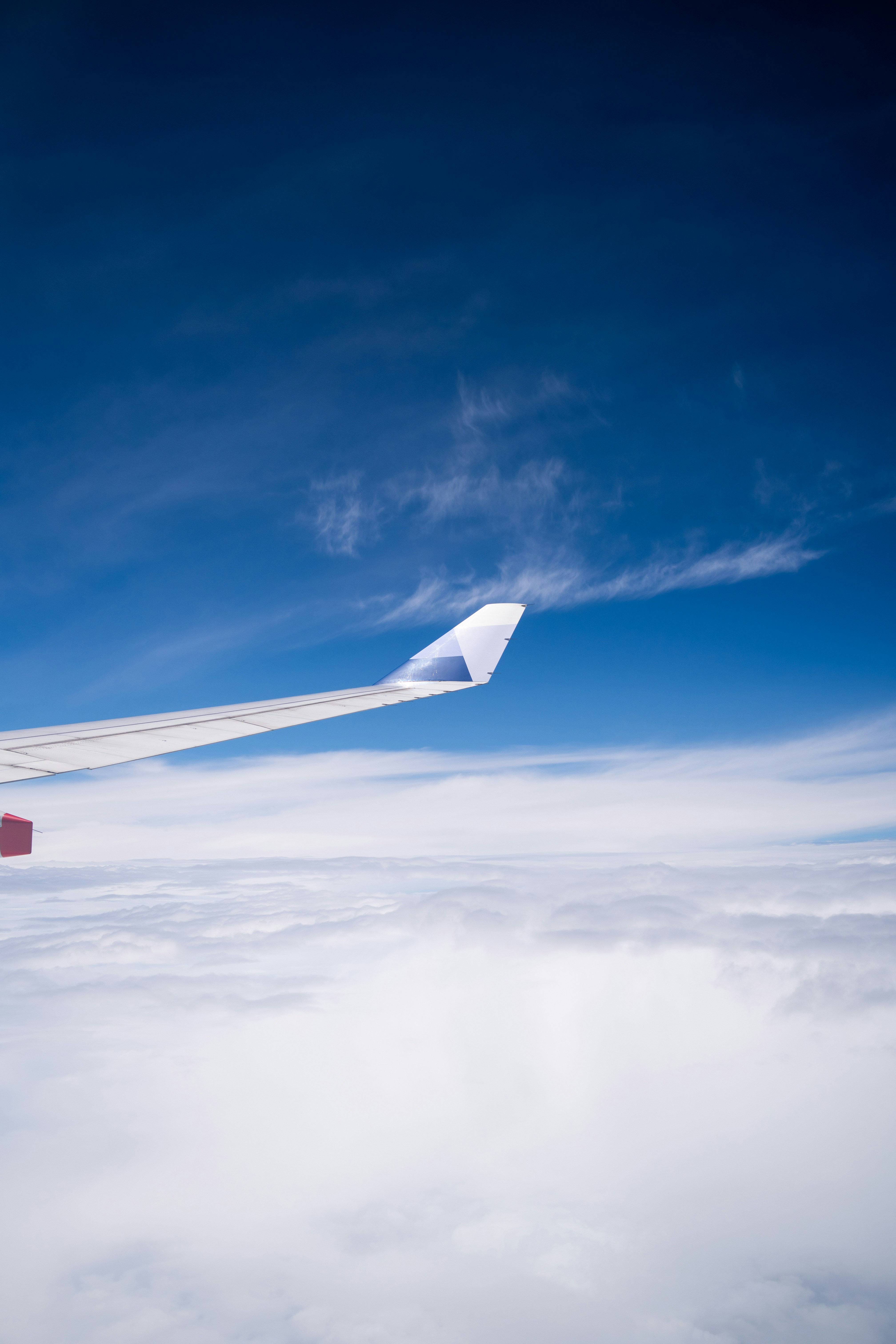Airplane wing extending over a sea of clouds under a vast blue sky. The image captures the tranquility of high-altitude travel.