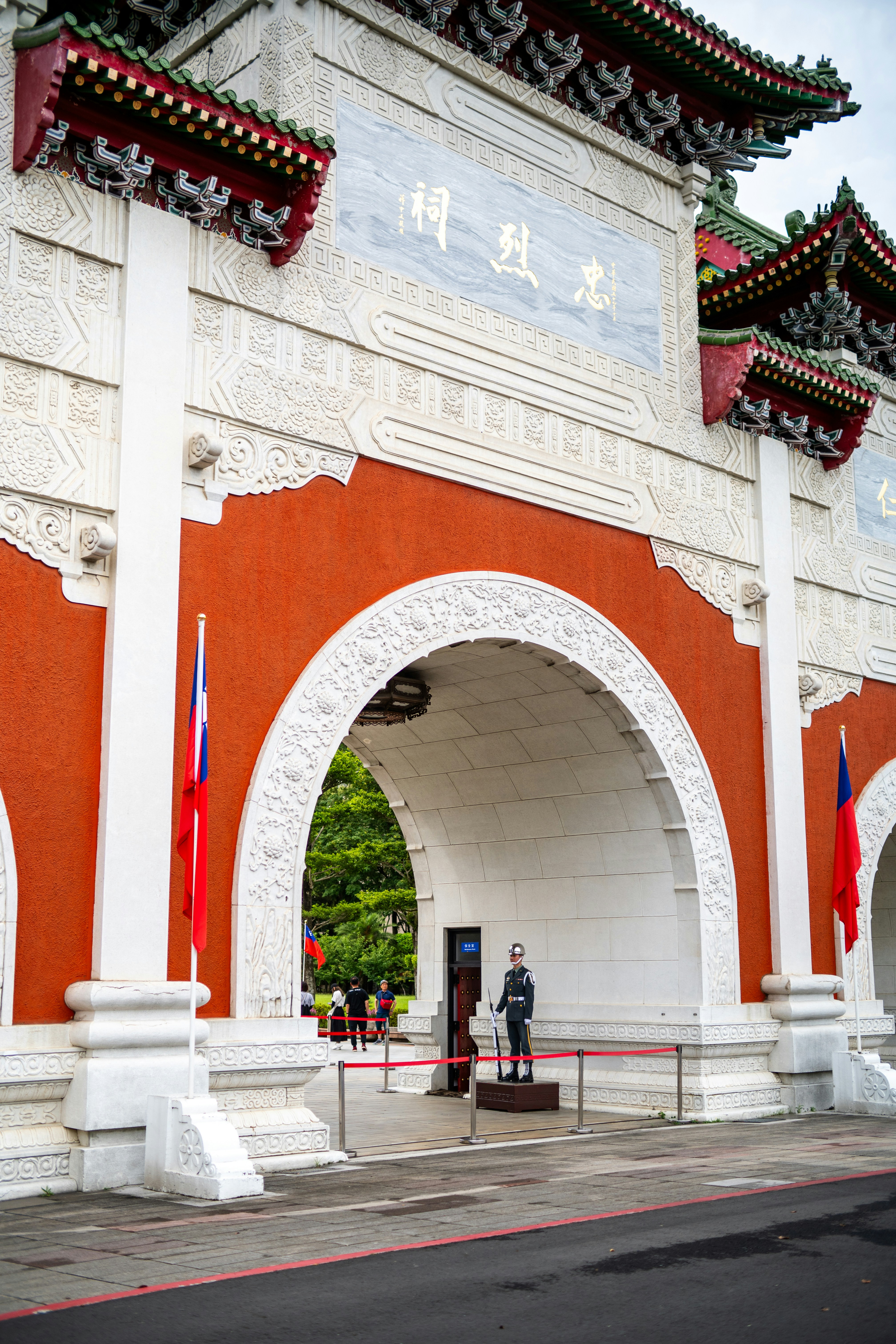Intricate archway adorned with traditional motifs, featuring a statue of a guard at its center. The vibrant orange backdrop contrasts with the ornate white carvings.