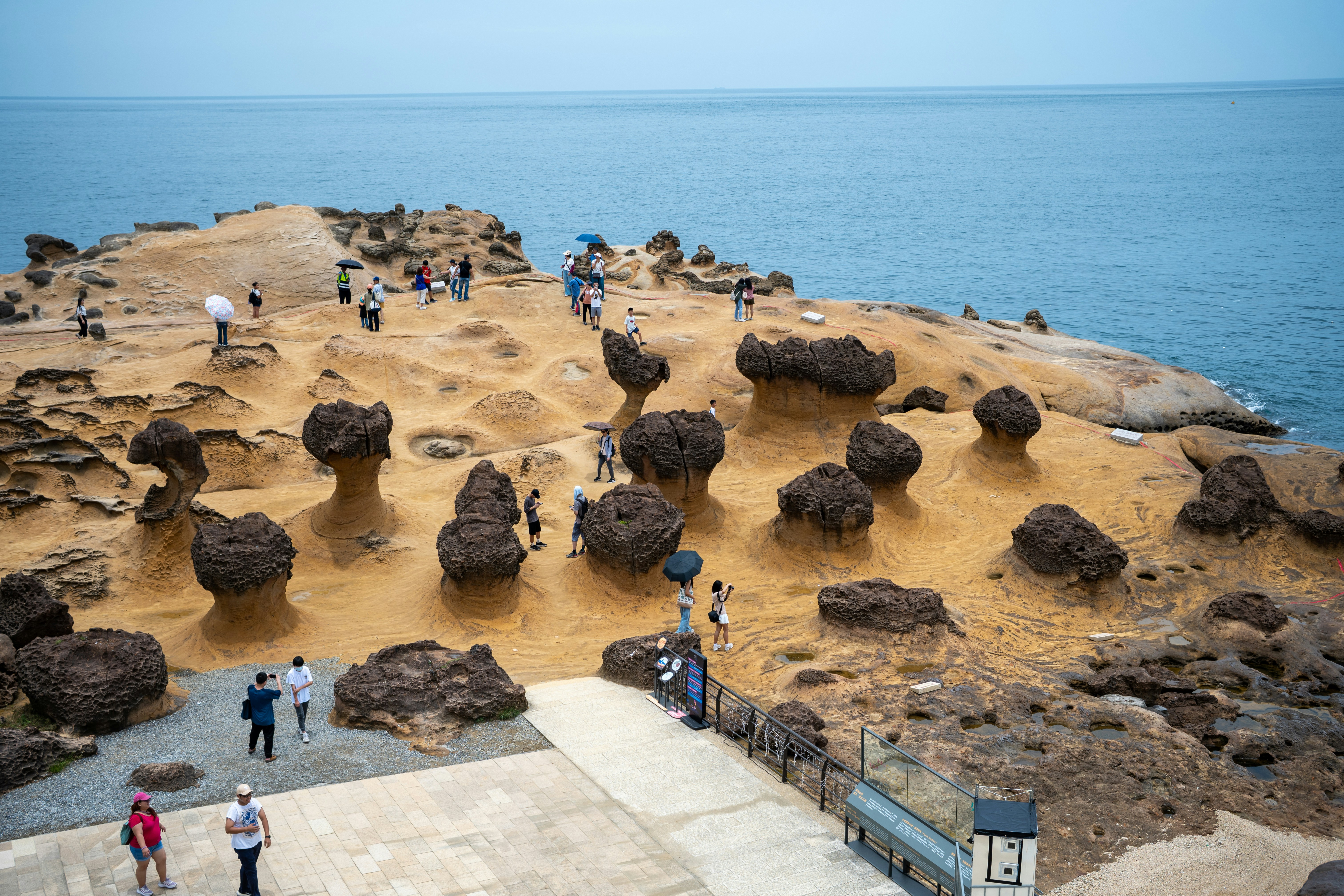 Tourists explore mushroom-shaped rocks by the ocean.