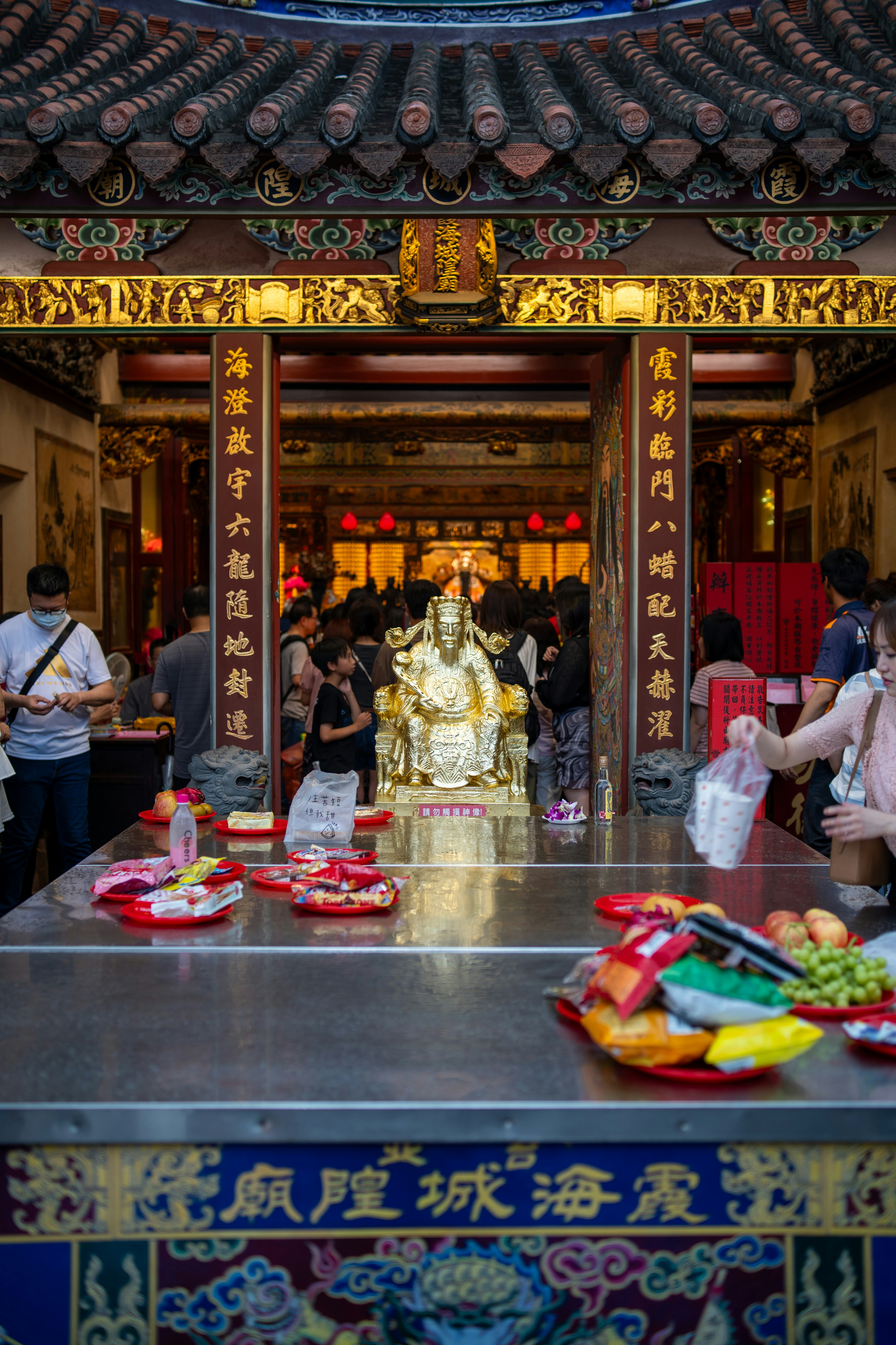 A vibrant temple scene featuring a golden deity surrounded by offerings and worshippers, showcasing cultural devotion and community engagement.