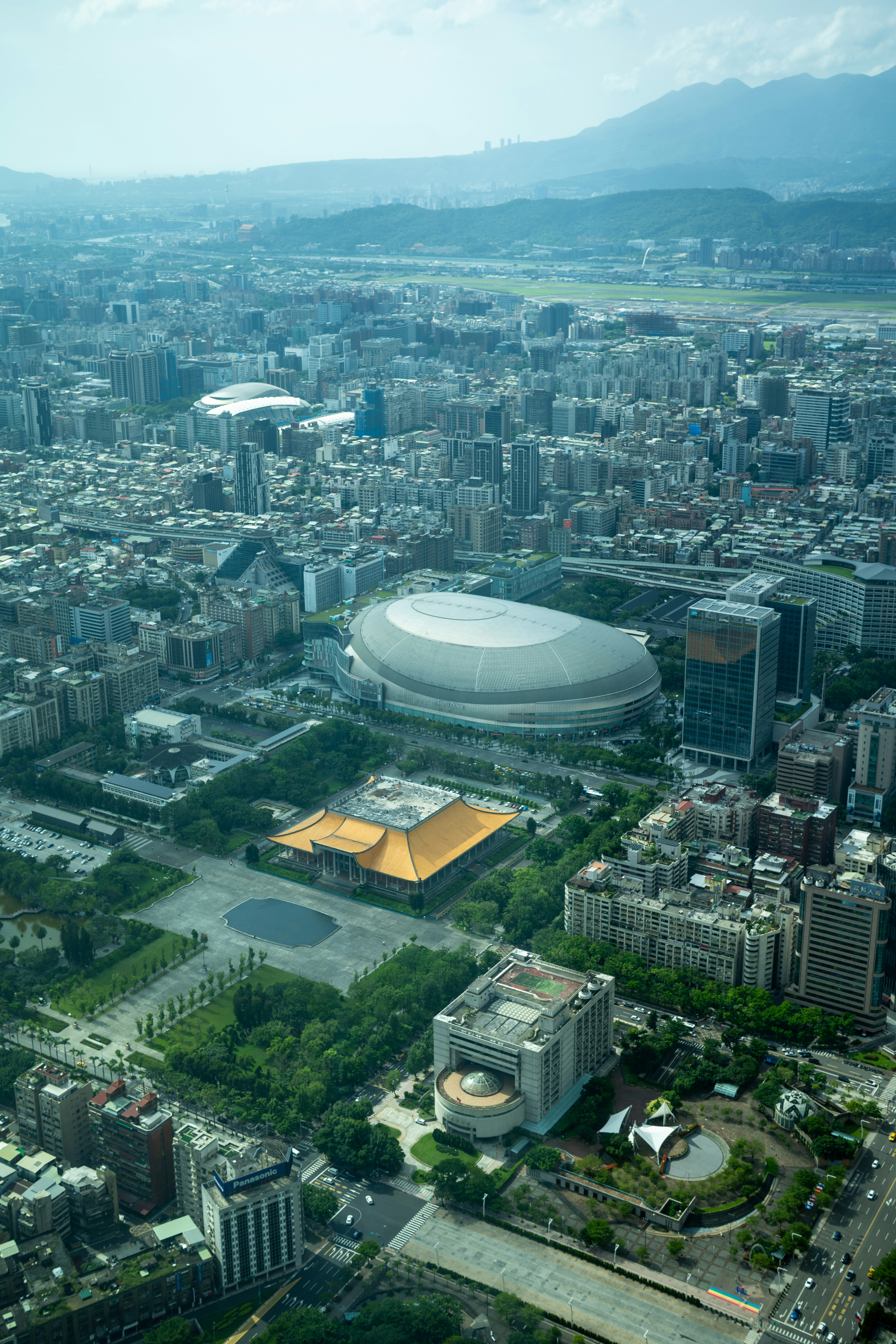 Aerial view of a vibrant cityscape showcasing a mix of modern architecture and green spaces, featuring notable buildings like a sports arena and cultural center.