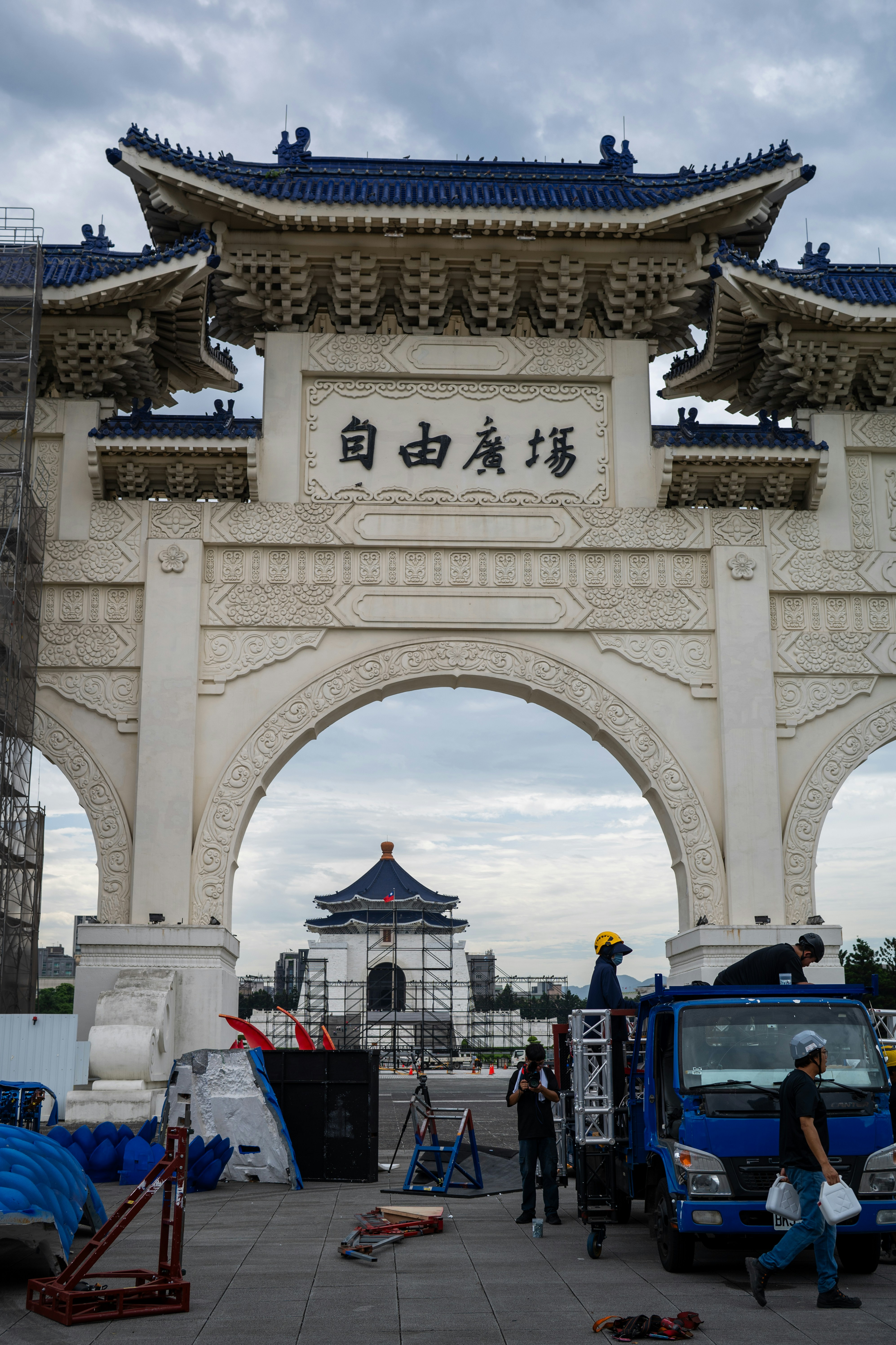 Intricate archway adorned with traditional motifs, framing a distant ceremonial structure amidst a bustling setup for an event.