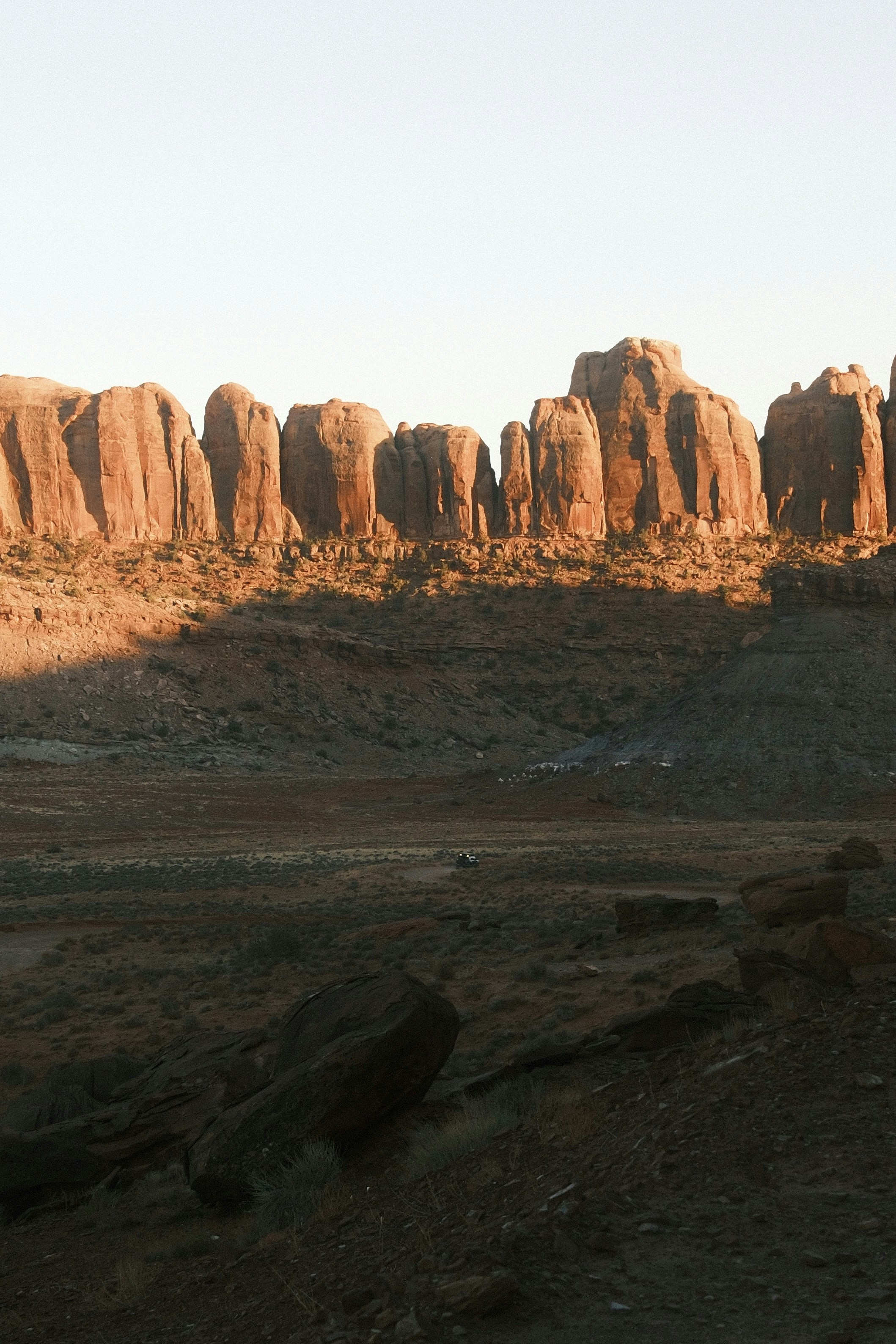 Sunset casts warm hues on towering rock formations, revealing the rugged textures of the desert terrain.