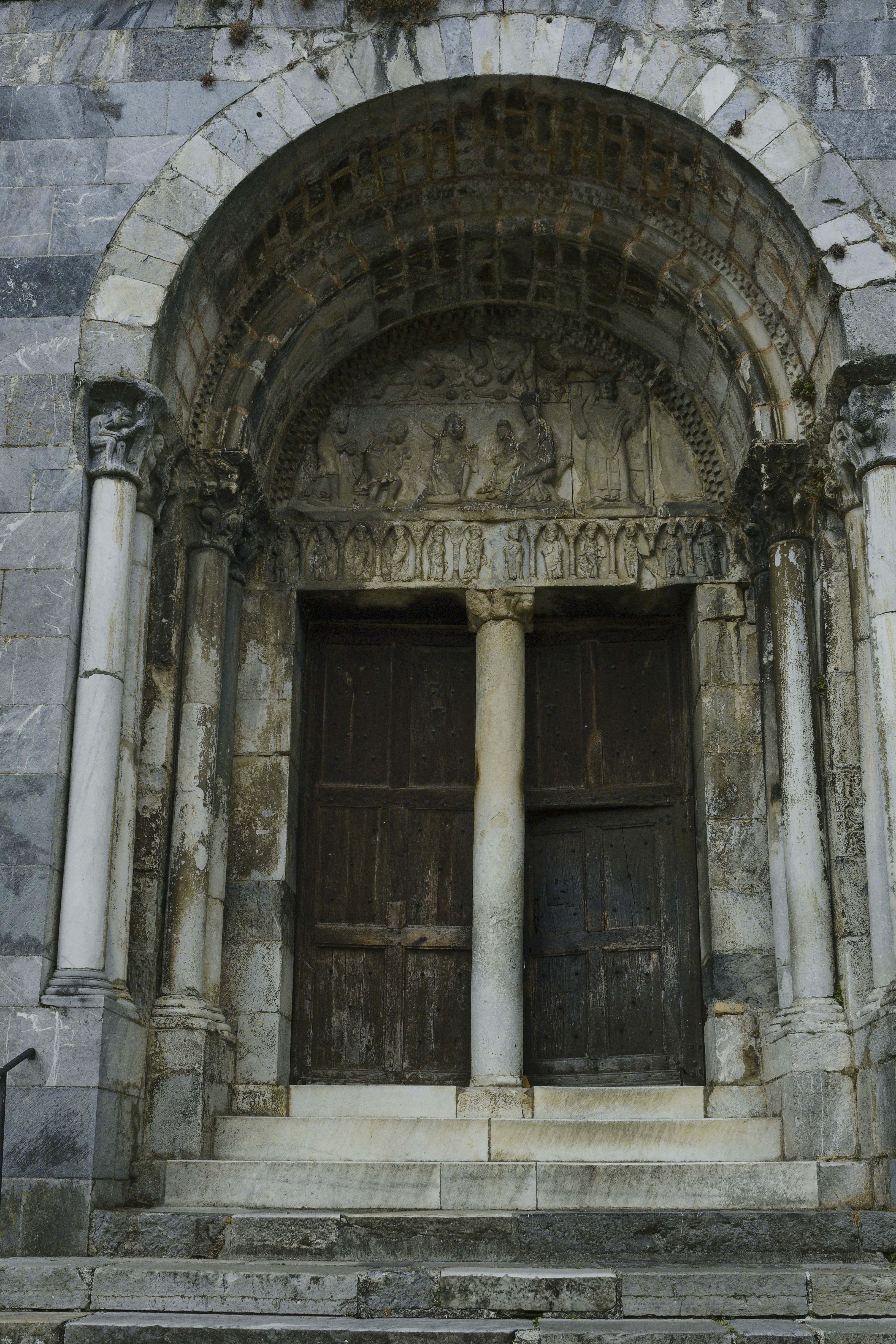 Historic stone entrance with intricate carvings and weathered wooden doors in an ancient church - A detailed view of a historic stone entrance featuring ornate carvings and large, weathered wooden doors. The architecture displays craftsmanship from a bygone era, evoking a sense of history. | A stone archway encompasses wooden church doors.