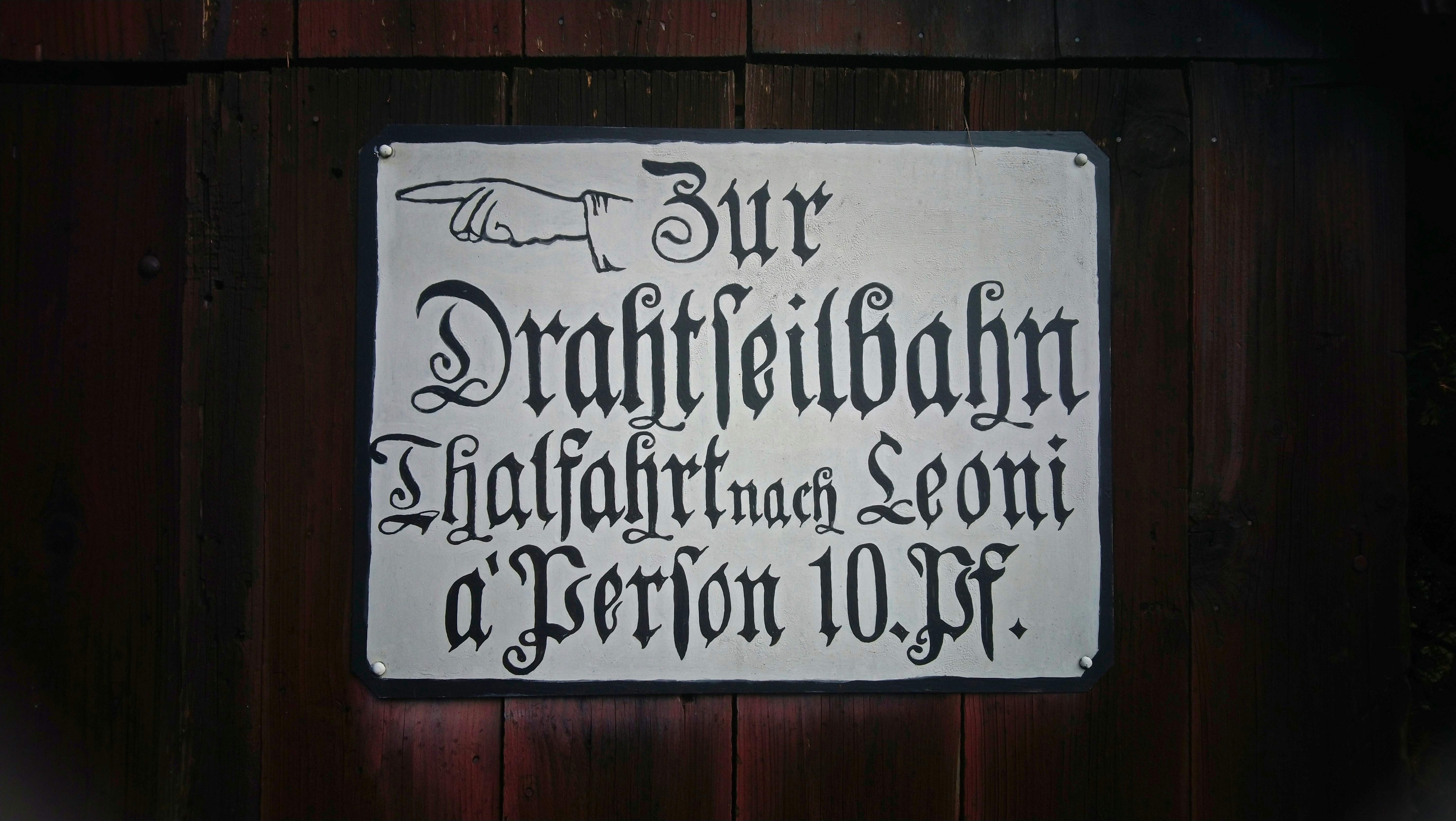 Vintage sign directing travelers to the Drahtseilbahn, featuring elegant calligraphy and a pointing hand. The sign evokes a sense of nostalgia and adventure.