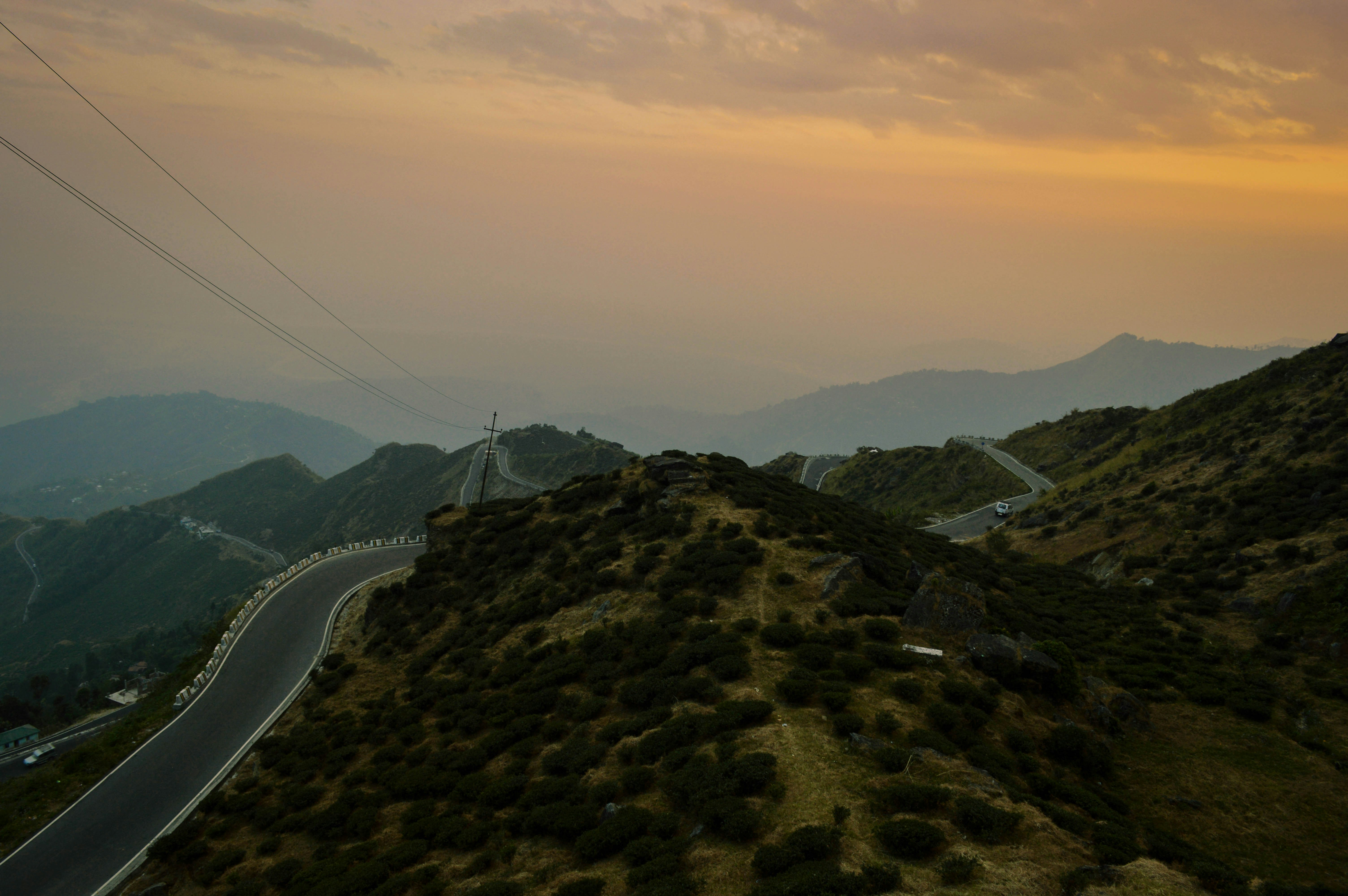 Winding road traversing a mountainous landscape at dusk, with a soft gradient of colors in the sky. The scene captures the harmony between nature and human engineering.