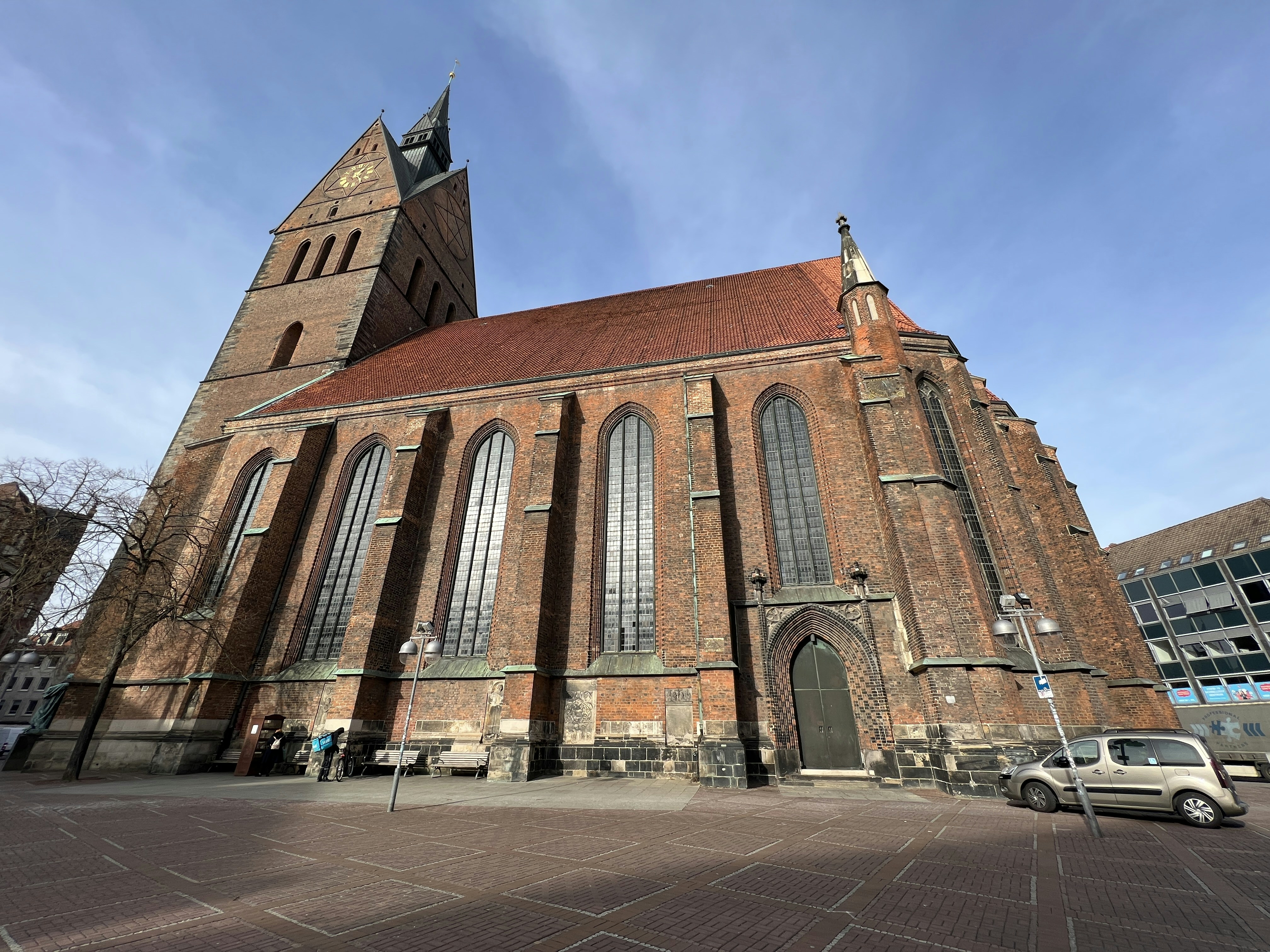 Majestic clock tower dominates the historic Markt square in Hanover's downtown area. | A large, brick church stands beneath a blue sky.