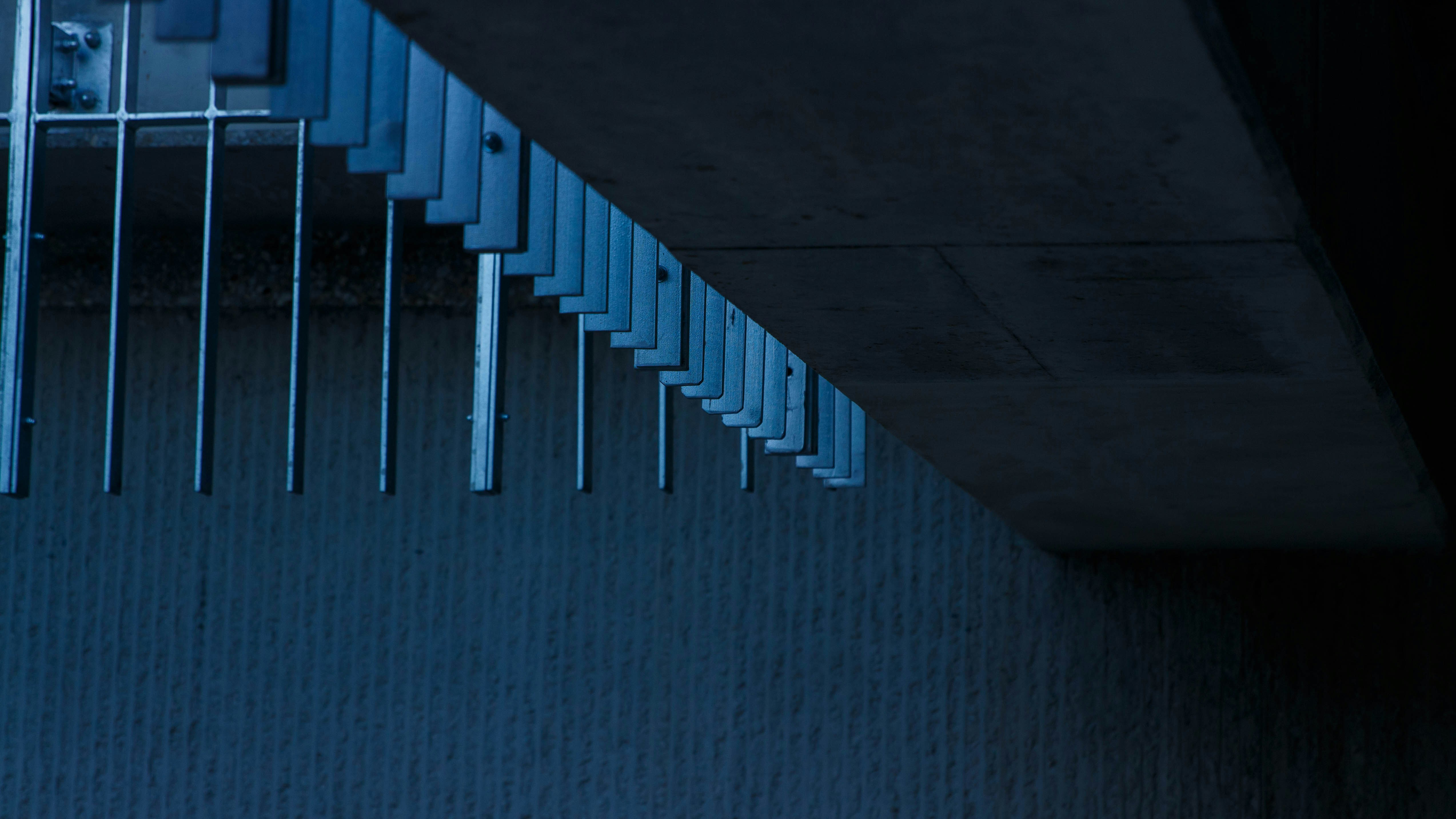 Abstract architectural elements featuring metallic rods and a concrete surface, emphasizing geometric patterns and interplay of light and shadow.