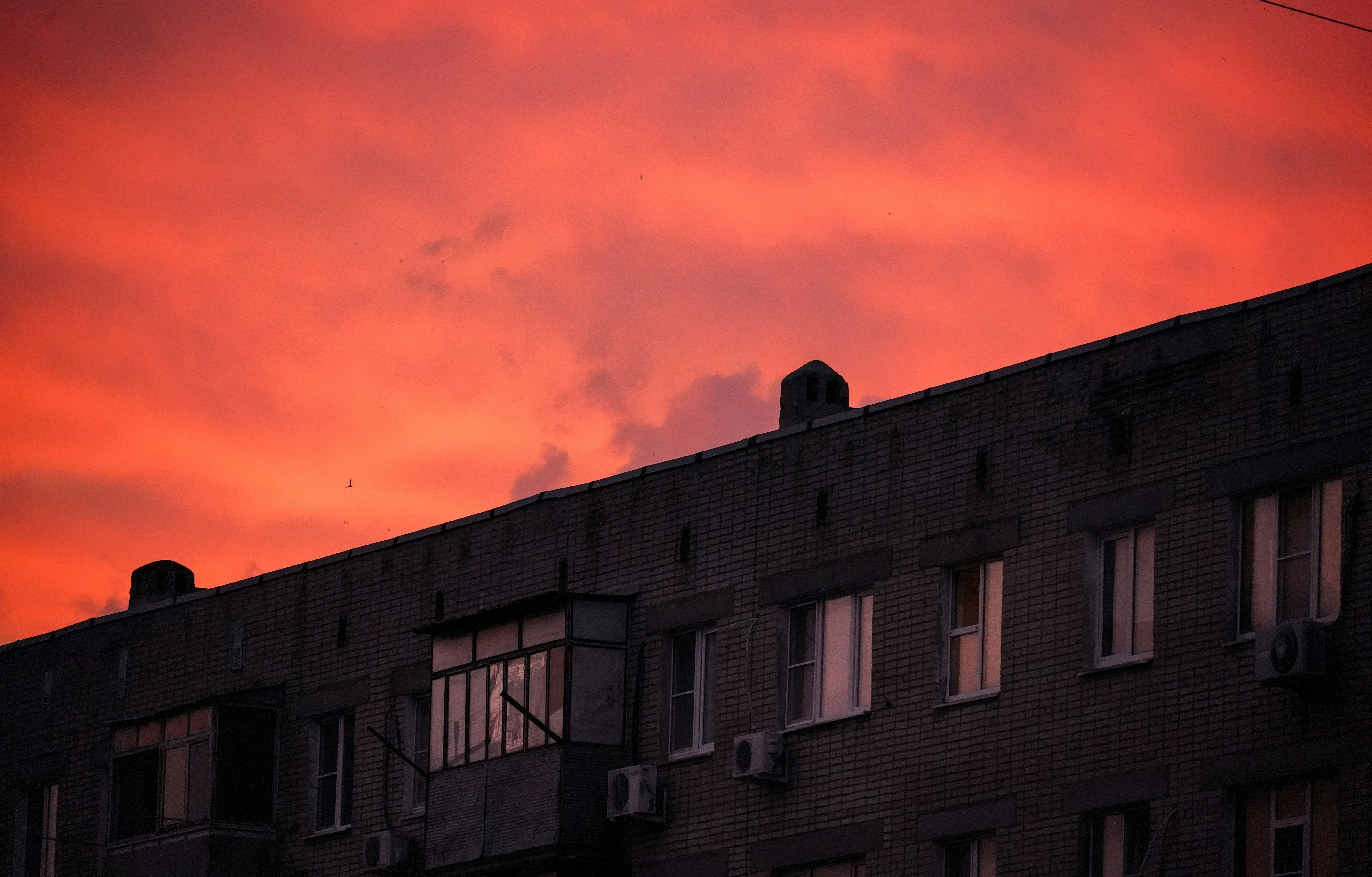 Dramatic sunset paints the sky orange and pink, silhouetting a residential building with distinct architectural features.
