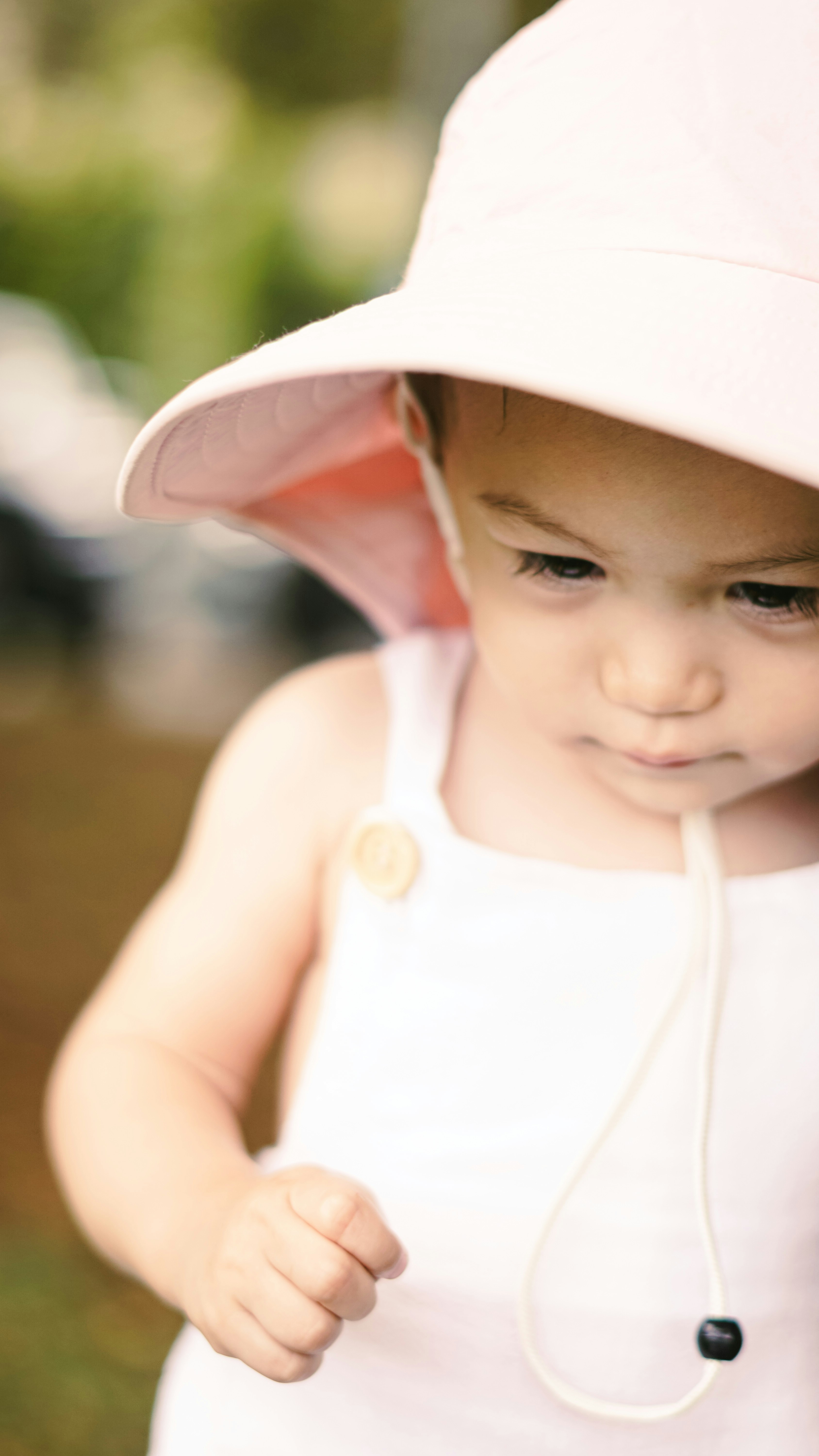 Medium close up of a toddler with pink hat. | A baby wearing a hat looks down pensively.