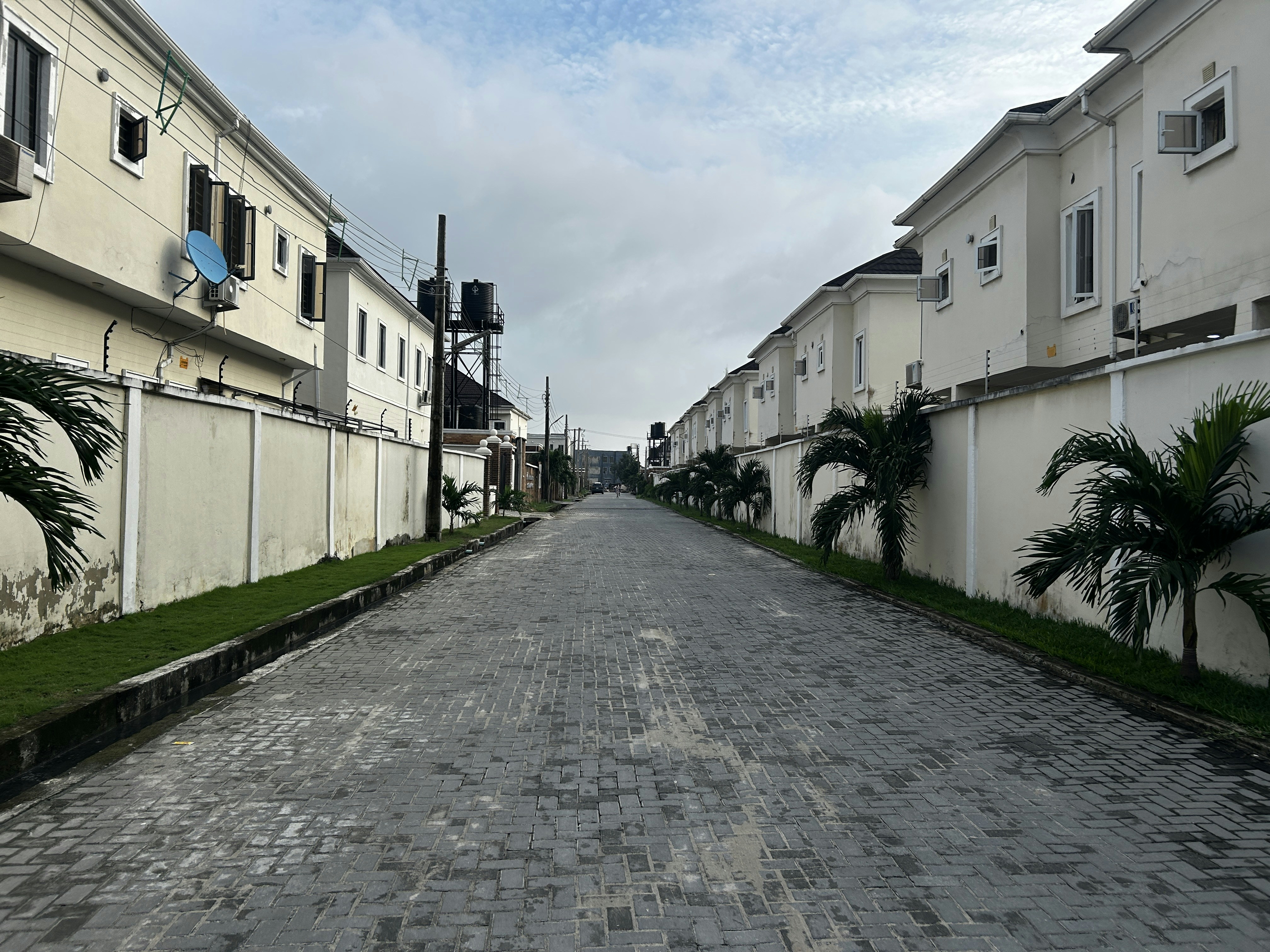 A tranquil street flanked by modern residential buildings, featuring neatly paved stones and lush greenery along the sides.