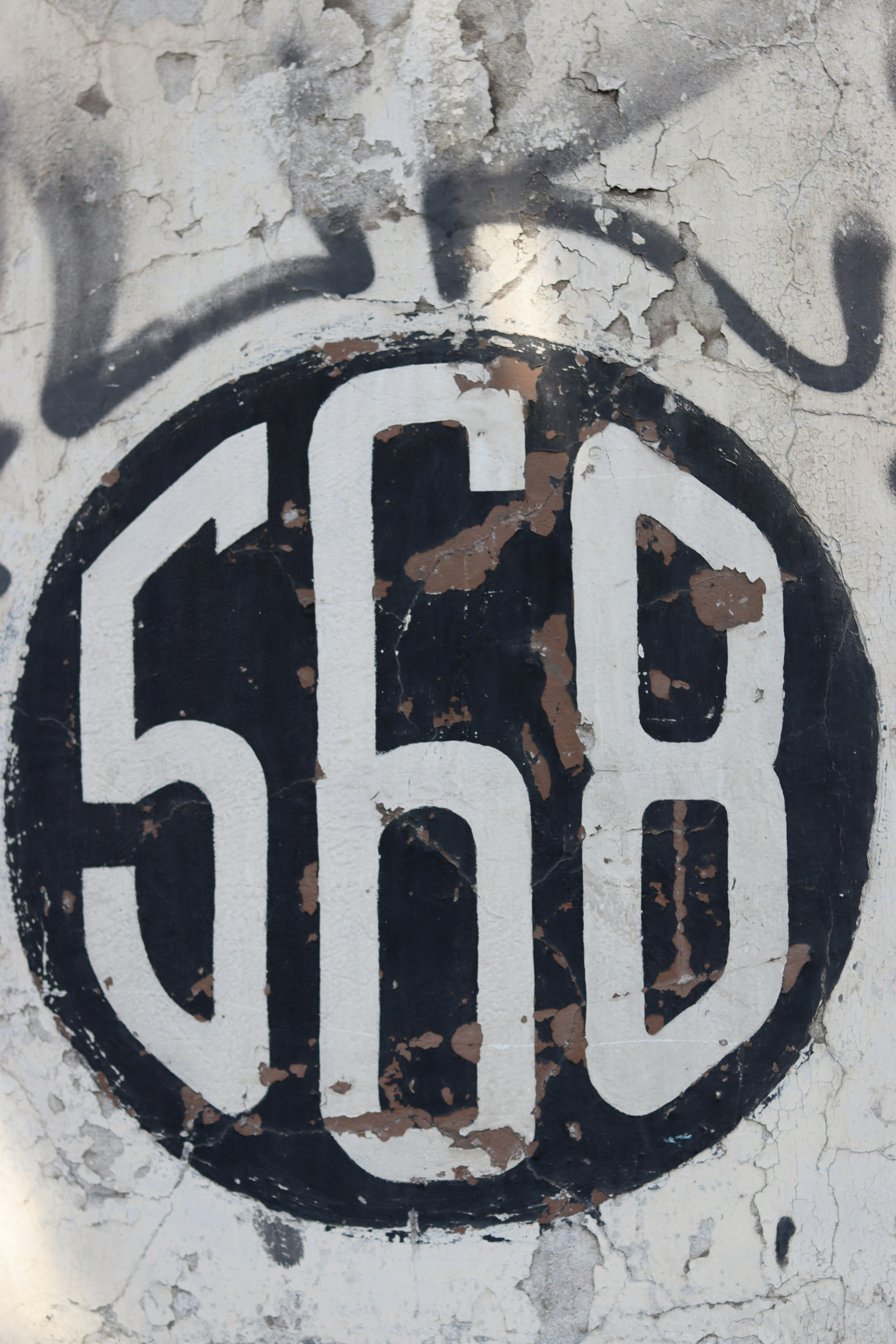 Faded black and white circular emblem featuring the number '568' against a cracked wall, showcasing urban decay and history.