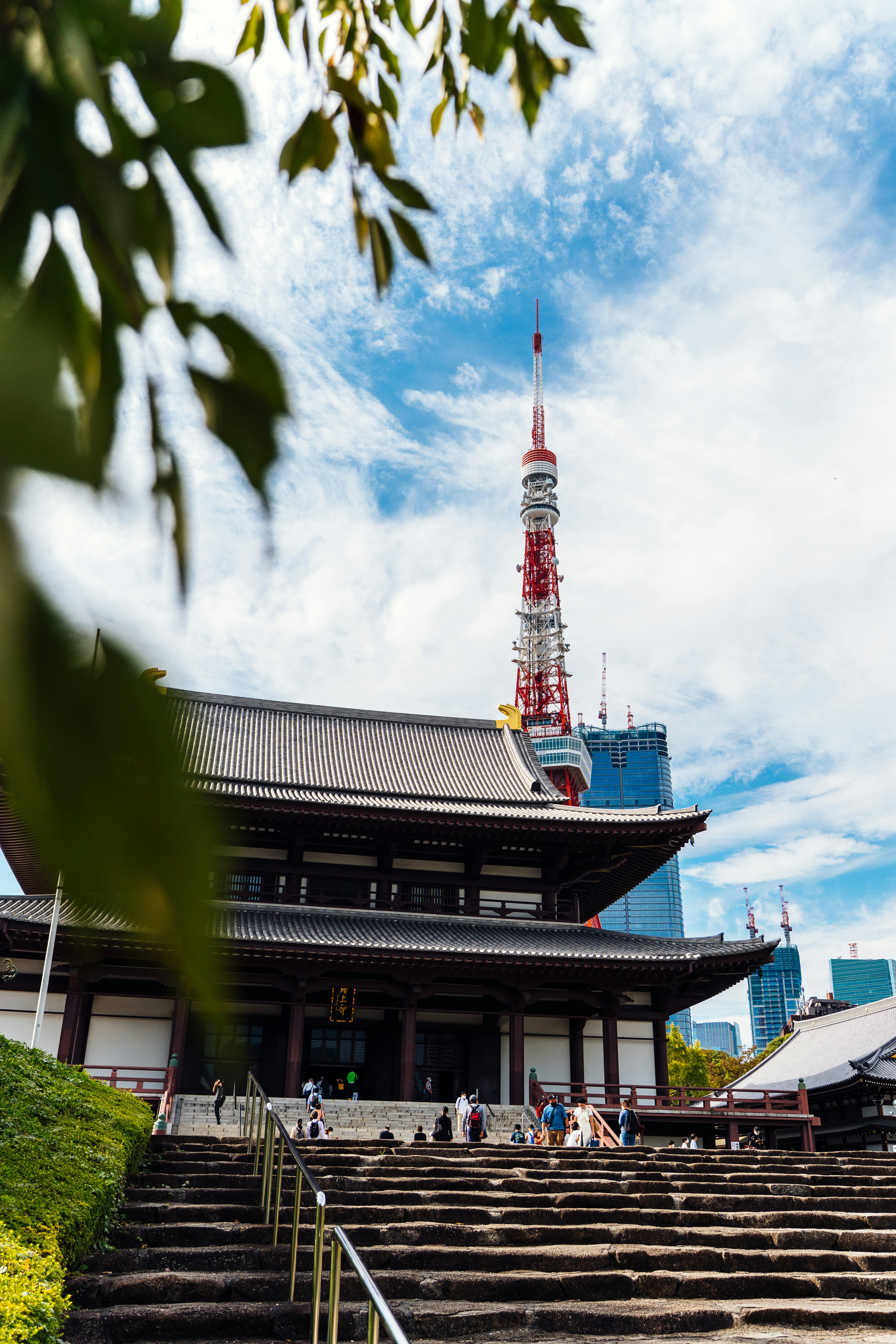 Historic temple steps leading to a traditional structure, framed by lush greenery and the Tokyo Tower in the background. 
