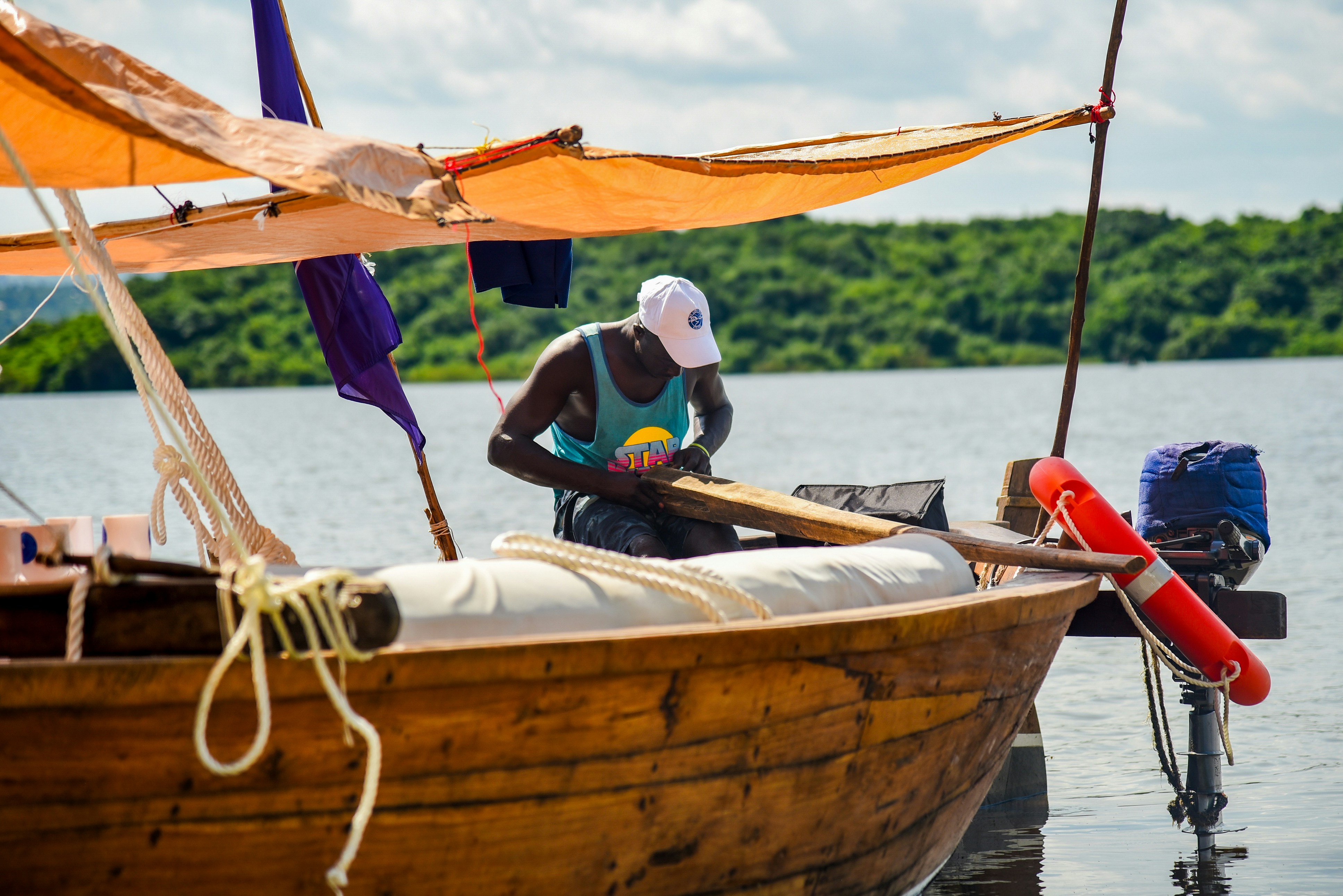 A man works on a boat at the water's edge.
