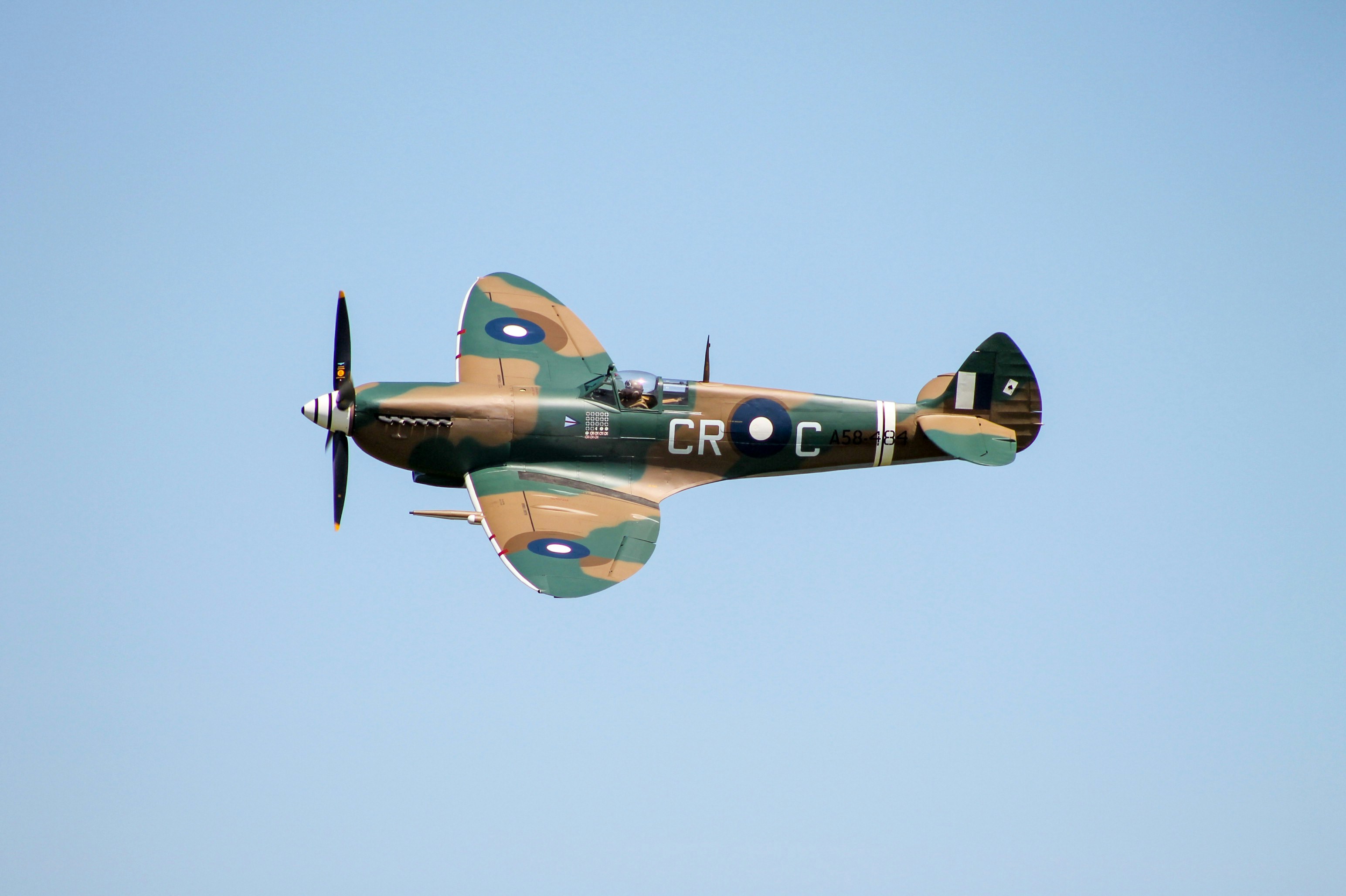 A powerful glimpse into aviation history — a World War II aircraft preserved in detail, capturing the essence of wartime engineering and design. | A camouflaged spitfire flies in the clear sky.