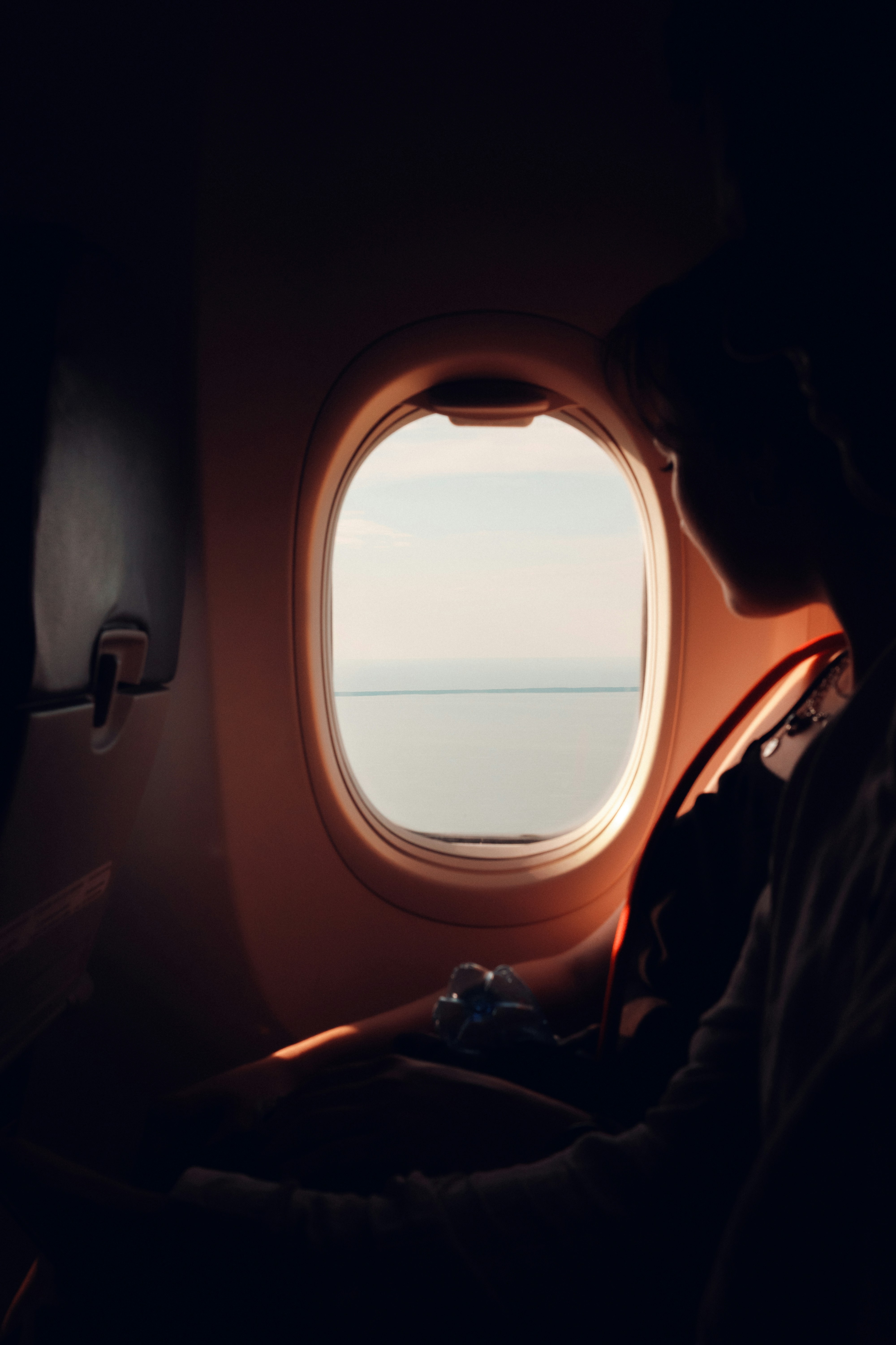 Passenger gazing out of an airplane window, overlooking a serene expanse of water under a clear sky.