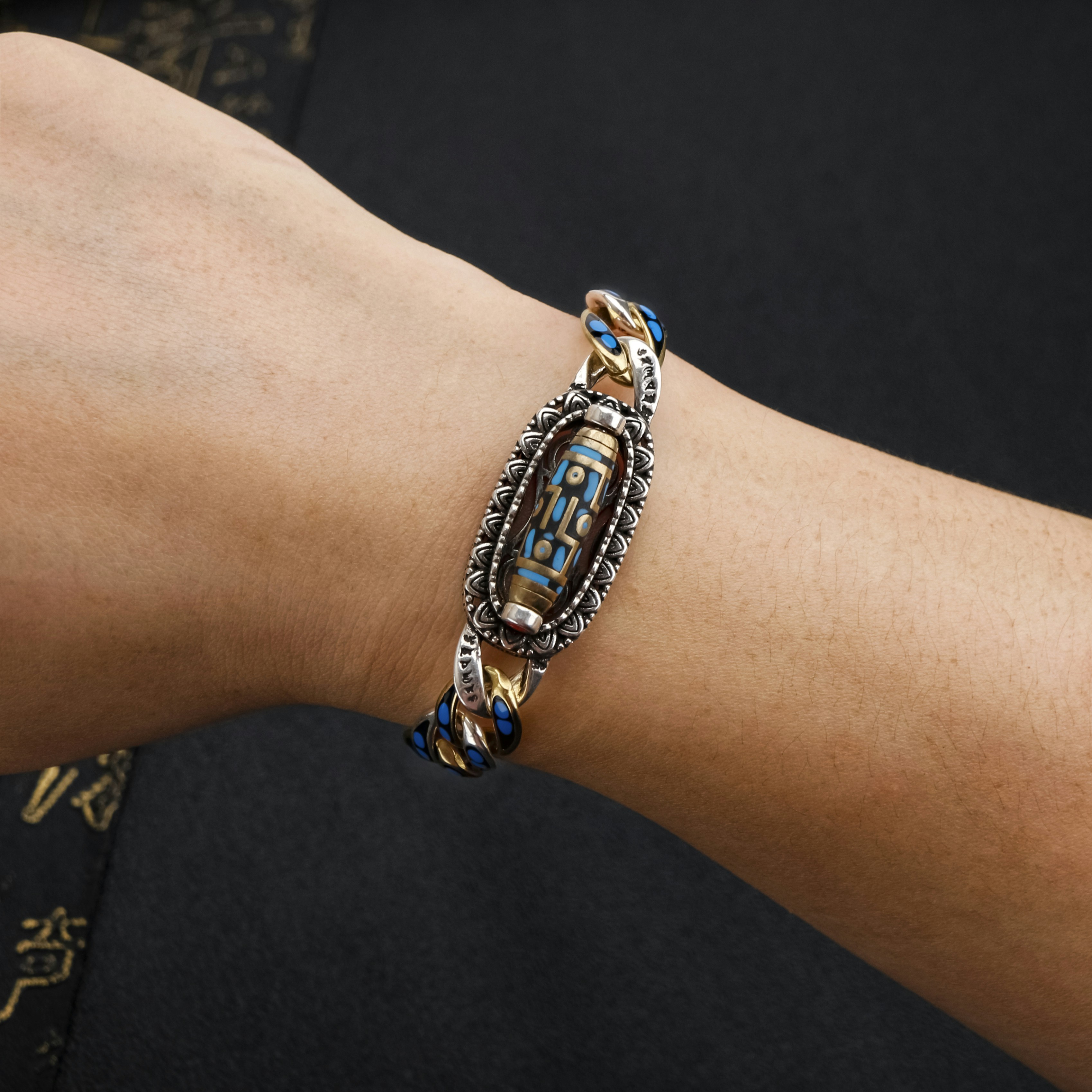 Intricate silver bracelet featuring a central decorative stone, elegantly worn on a wrist against a dark background.