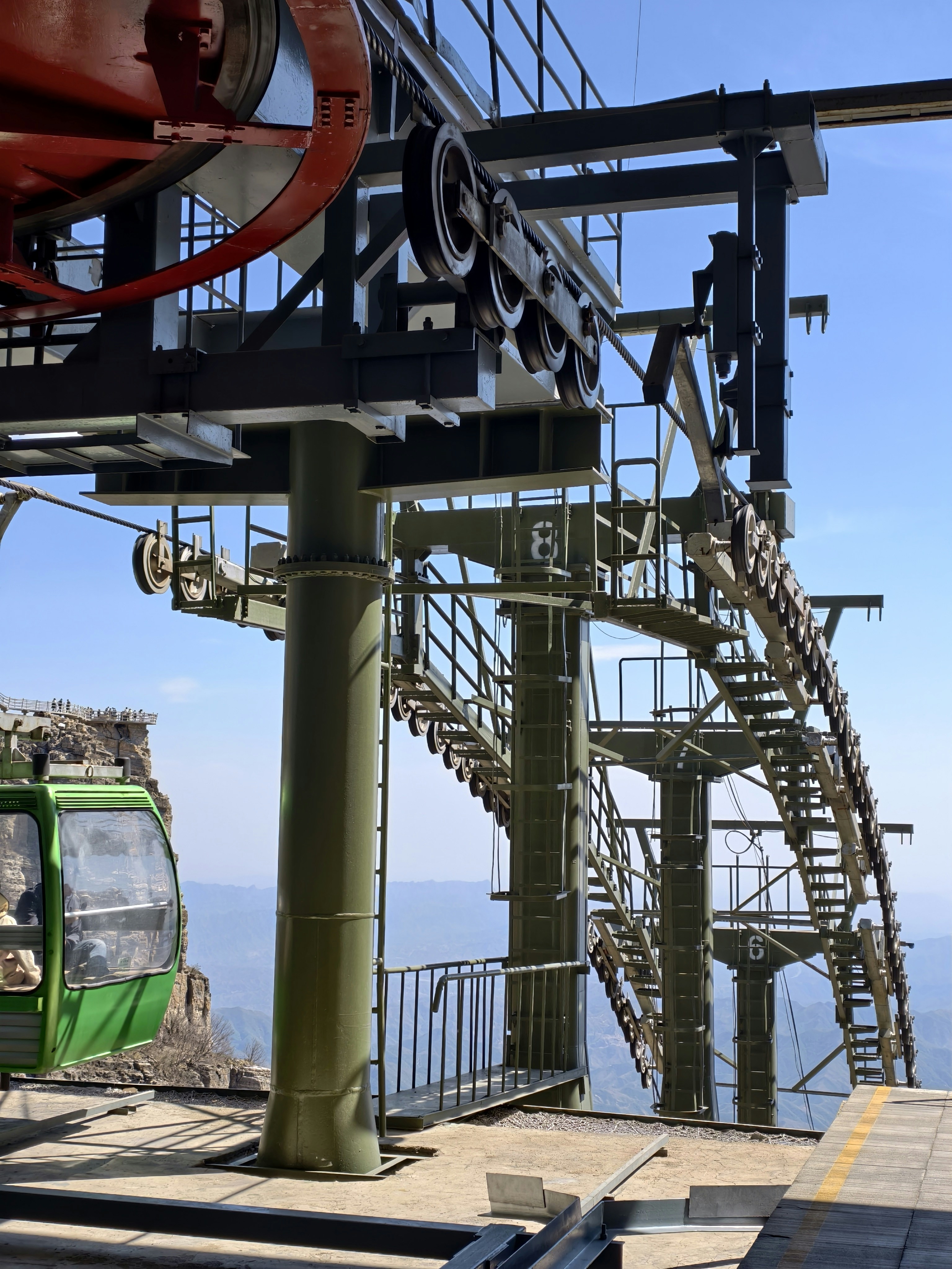 Cable car station with a green gondola suspended above a mountainous landscape, showcasing the intricate machinery and scenic backdrop. 