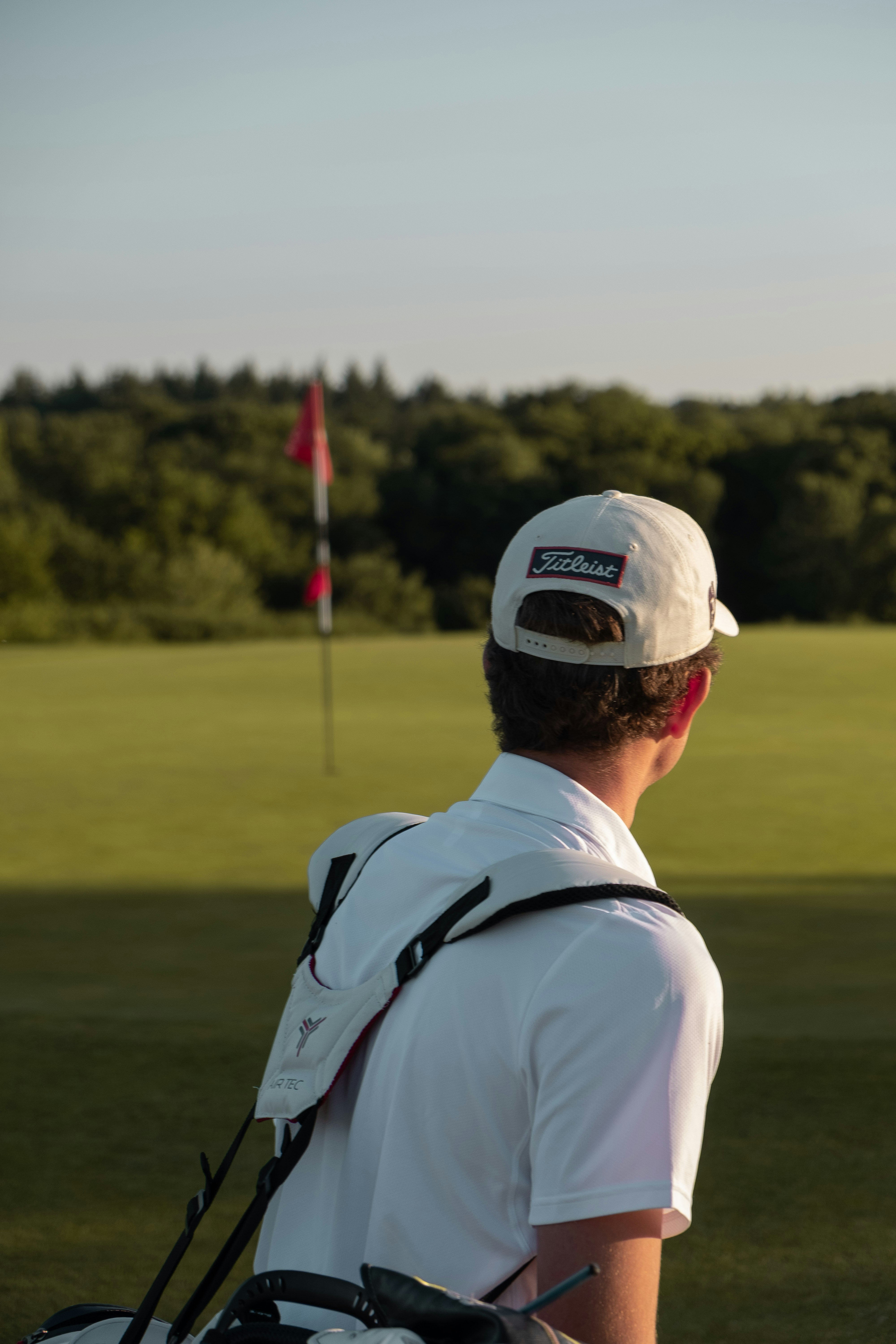 Golfer in a Titleist cap gazes towards the flag on a lush green golf course, embodying focus and determination.