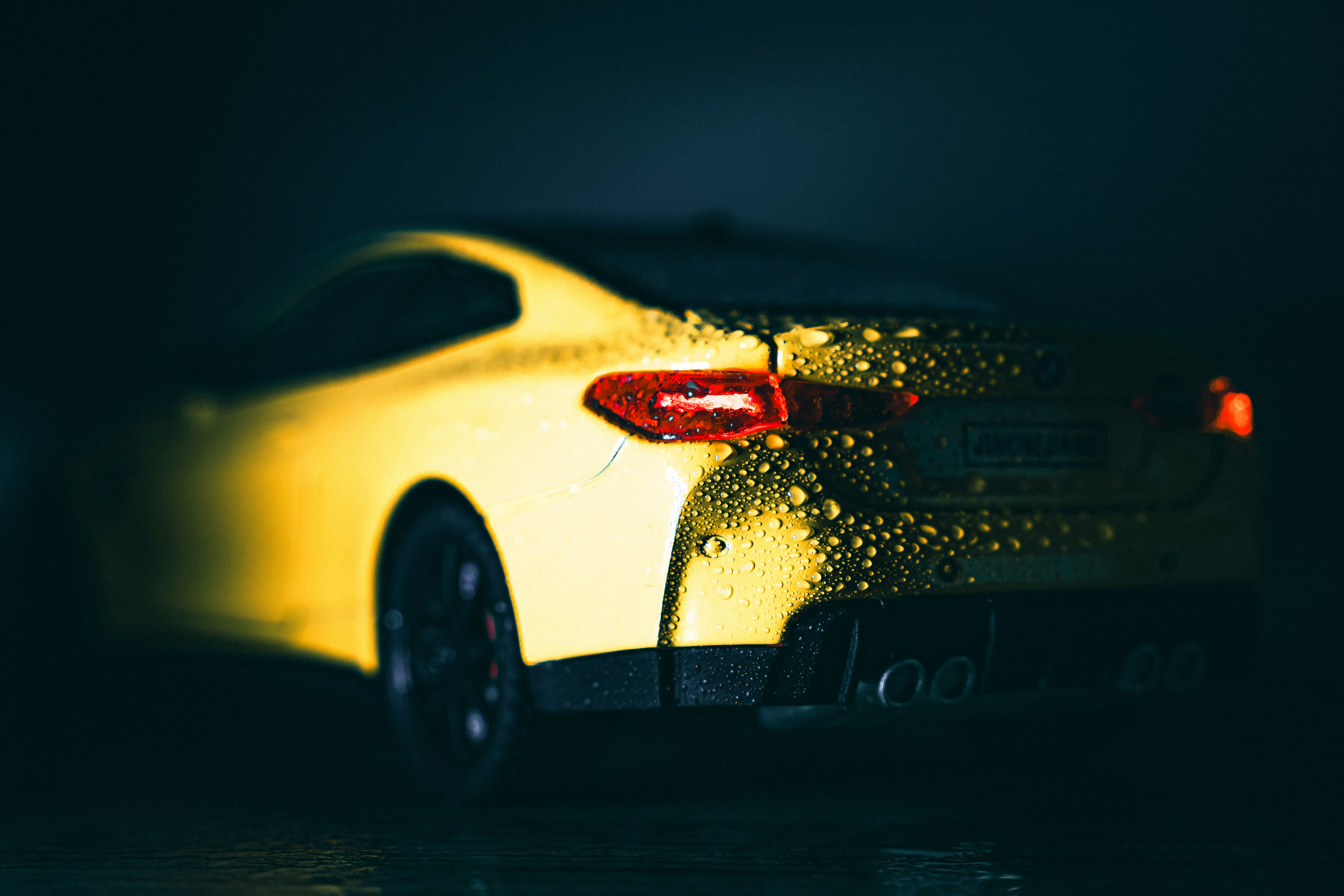 A close-up view of a yellow sports car model, adorned with droplets of water, set against a dark background.