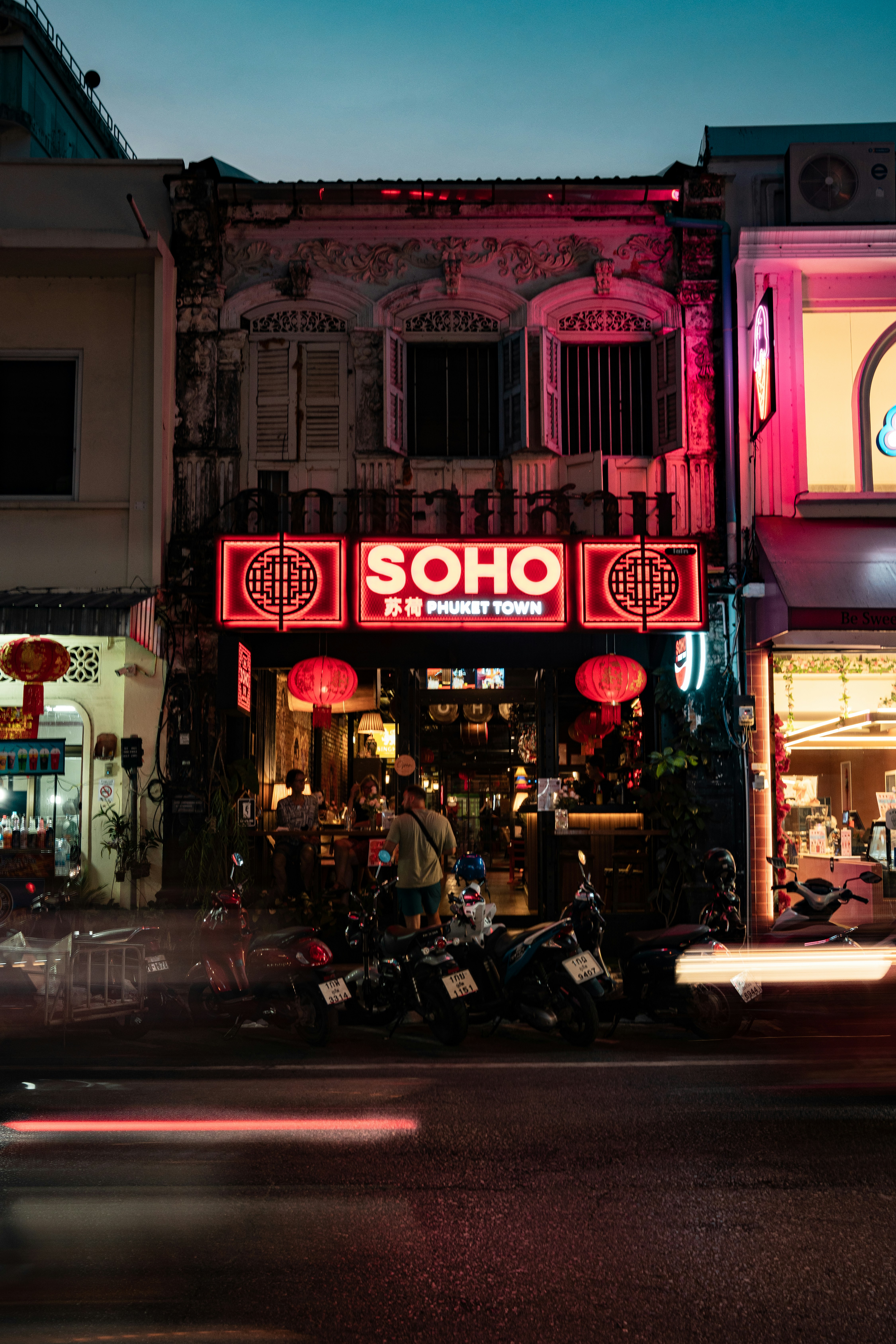 Illuminated storefront of SOHO in Phuket Town, featuring vibrant red signage and lanterns against a twilight backdrop.