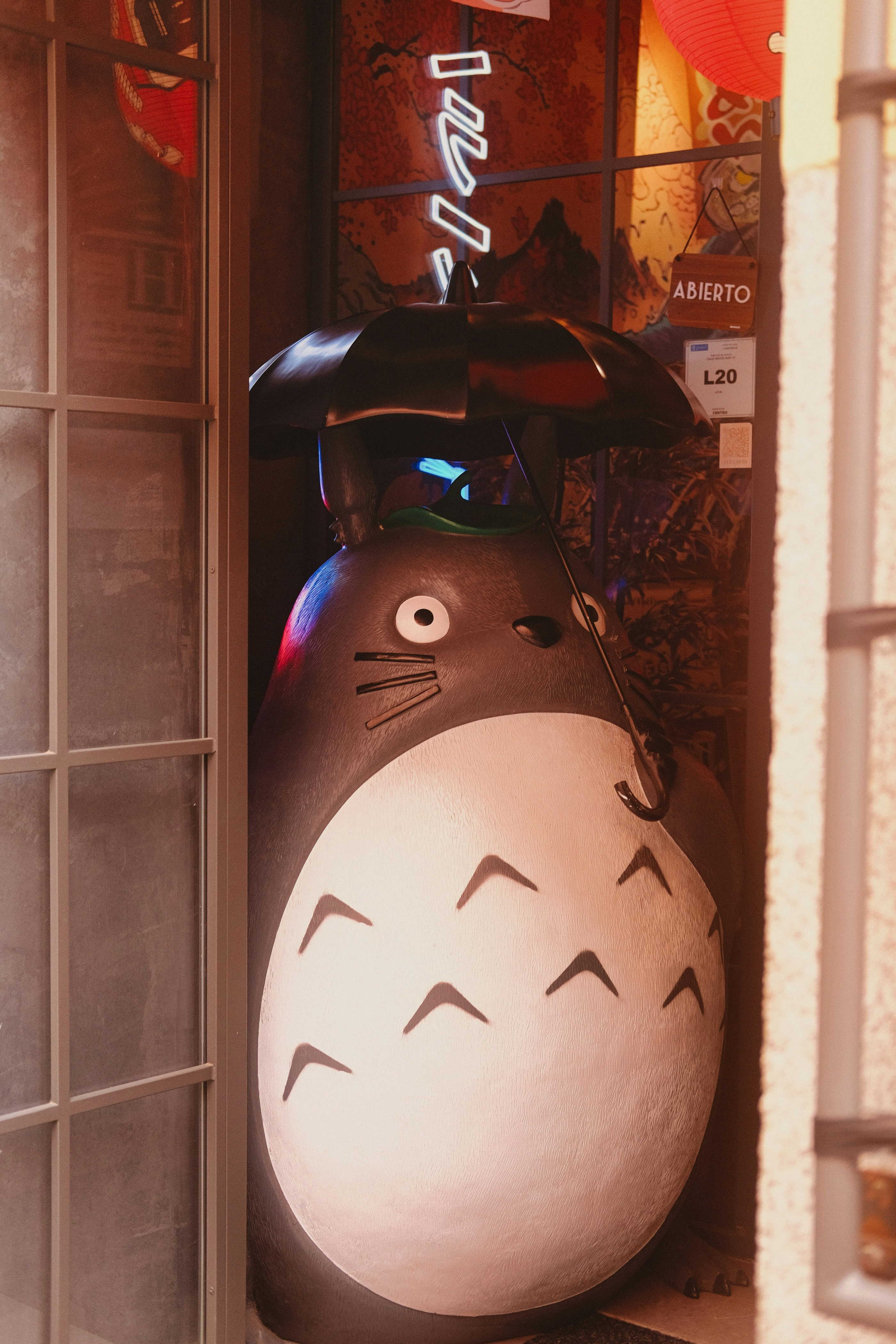 A totoro statue holds an umbrella in a window.