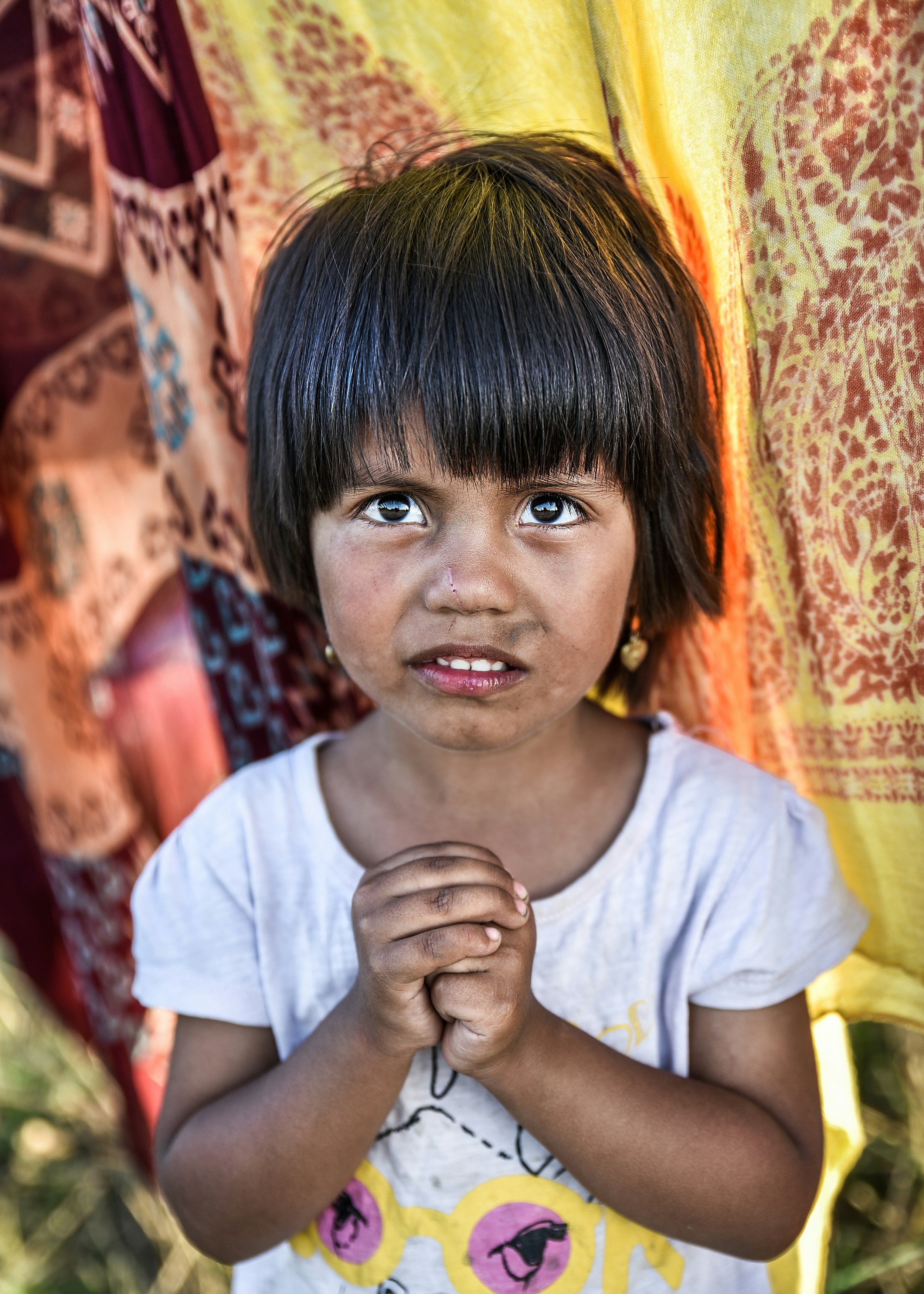 A young girl looks up, hands clasped together.