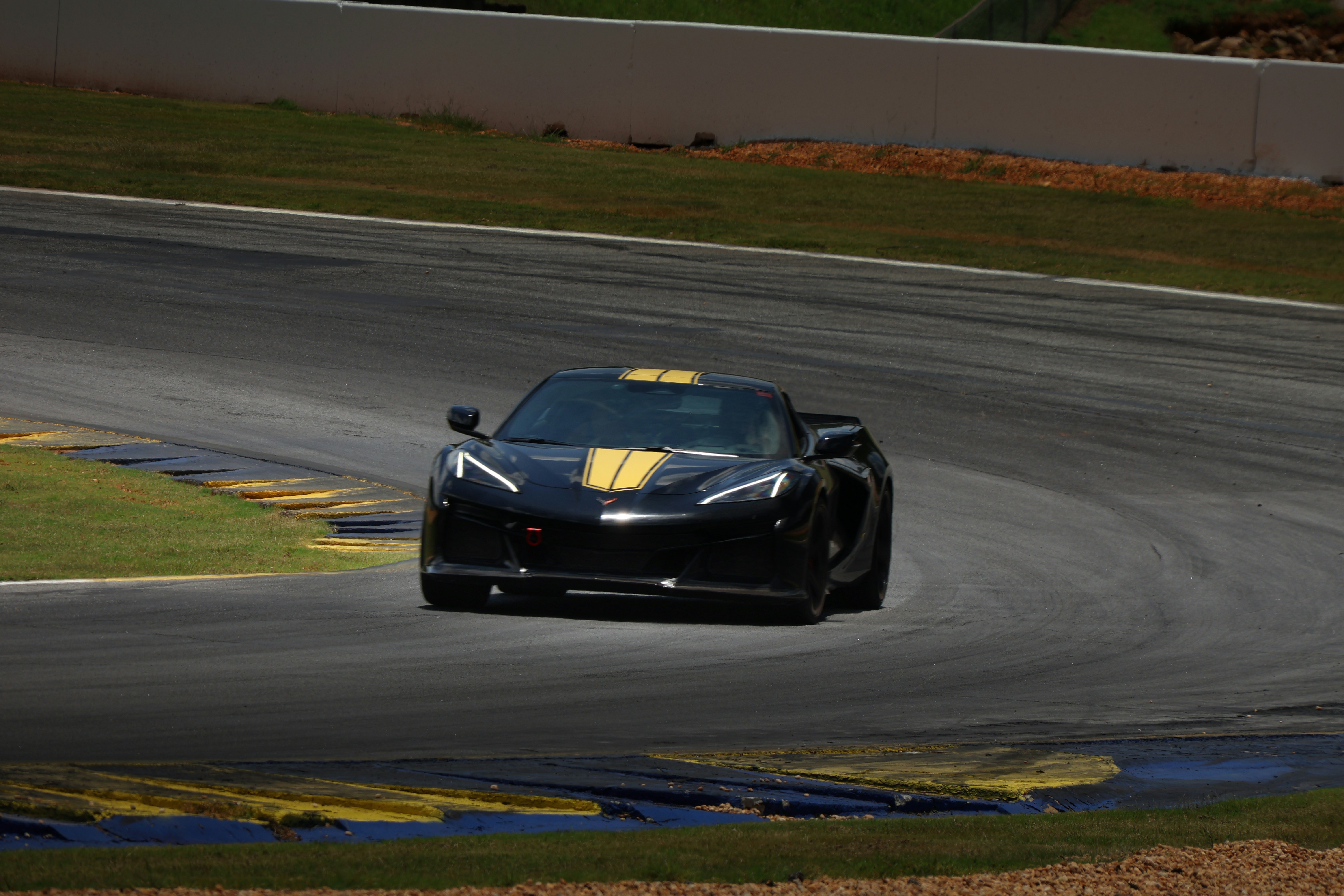 A sleek black sports car with yellow accents navigates a racetrack's sharp turn, showcasing its agility and design. The dynamic motion captures the essence of speed and engineering.