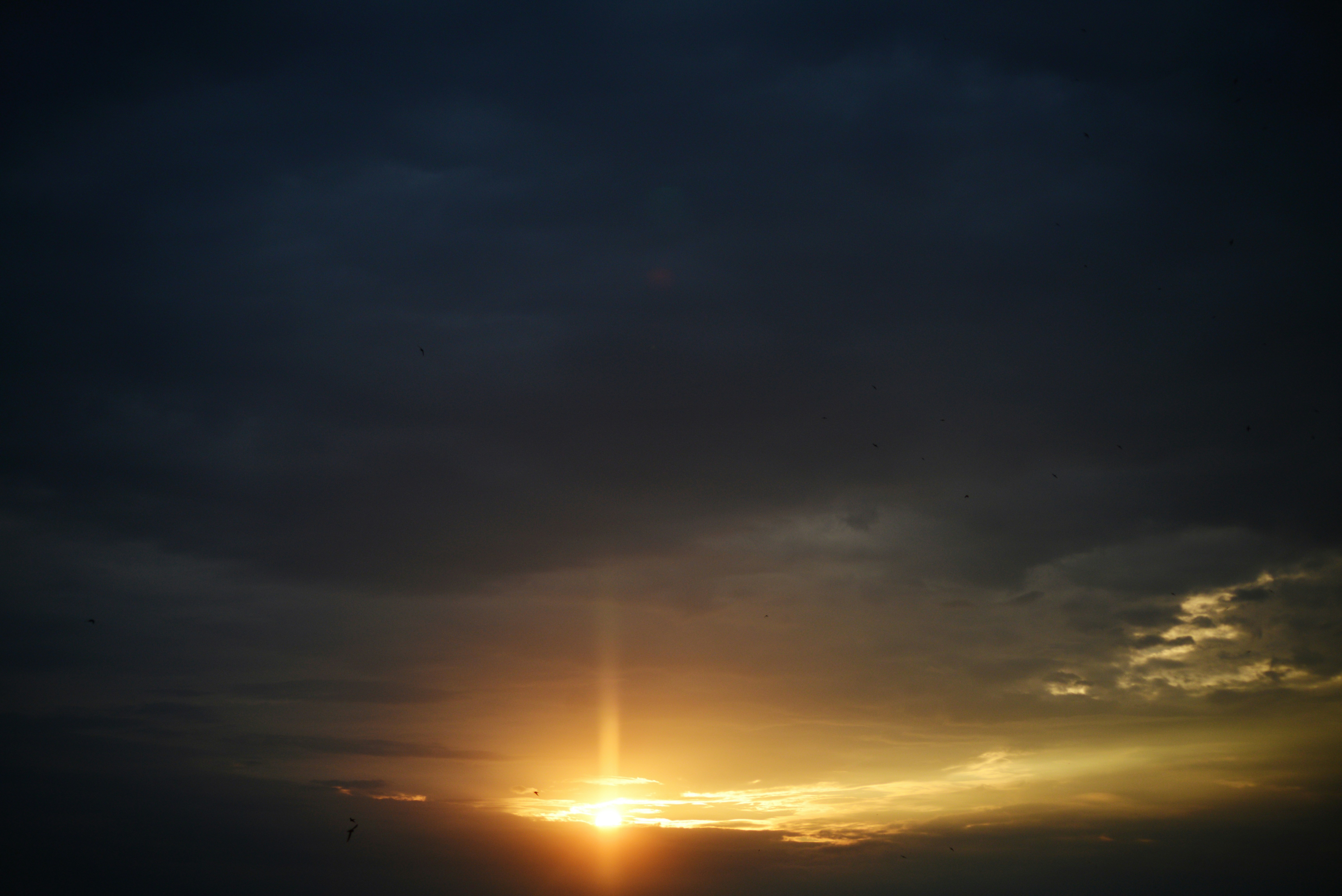 The sun shines through the dark and cloudy sky.