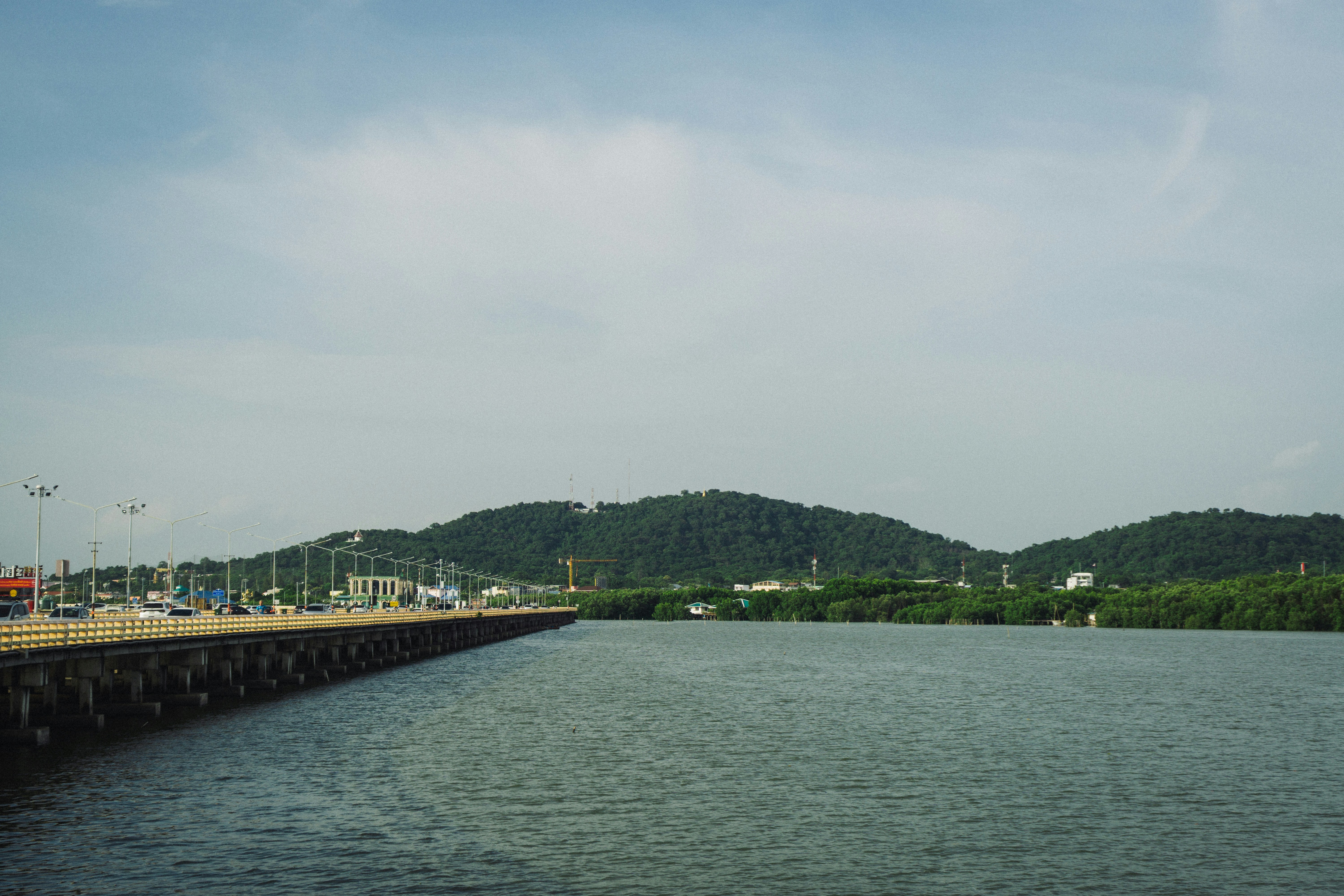 A bridge extends over water with a hill.