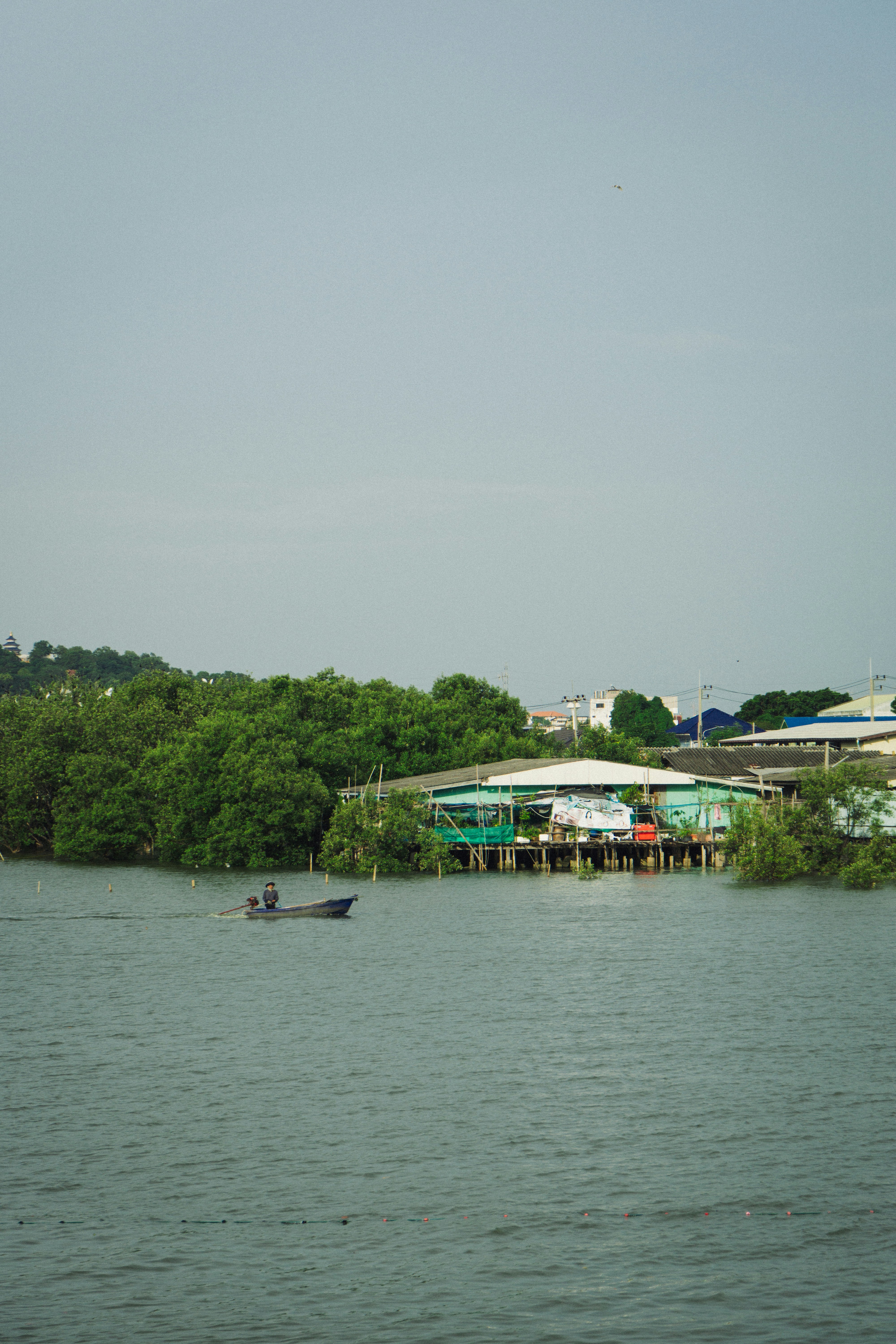 A lone fisherman navigates a small boat through calm waters, with lush mangroves and colorful structures in the background.